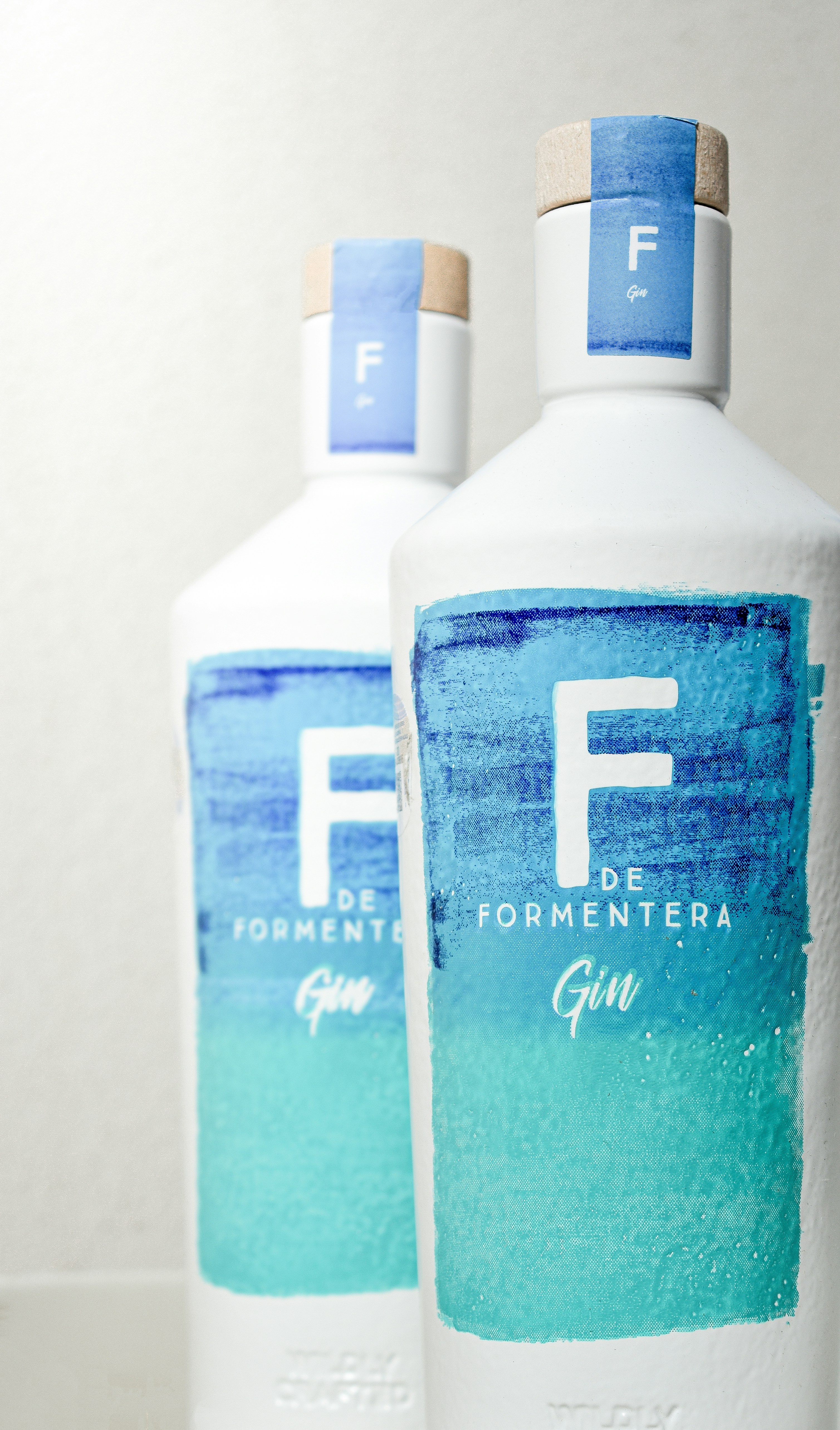 Two F de Formentera gin bottles with blue and turquoise labels against a light background.