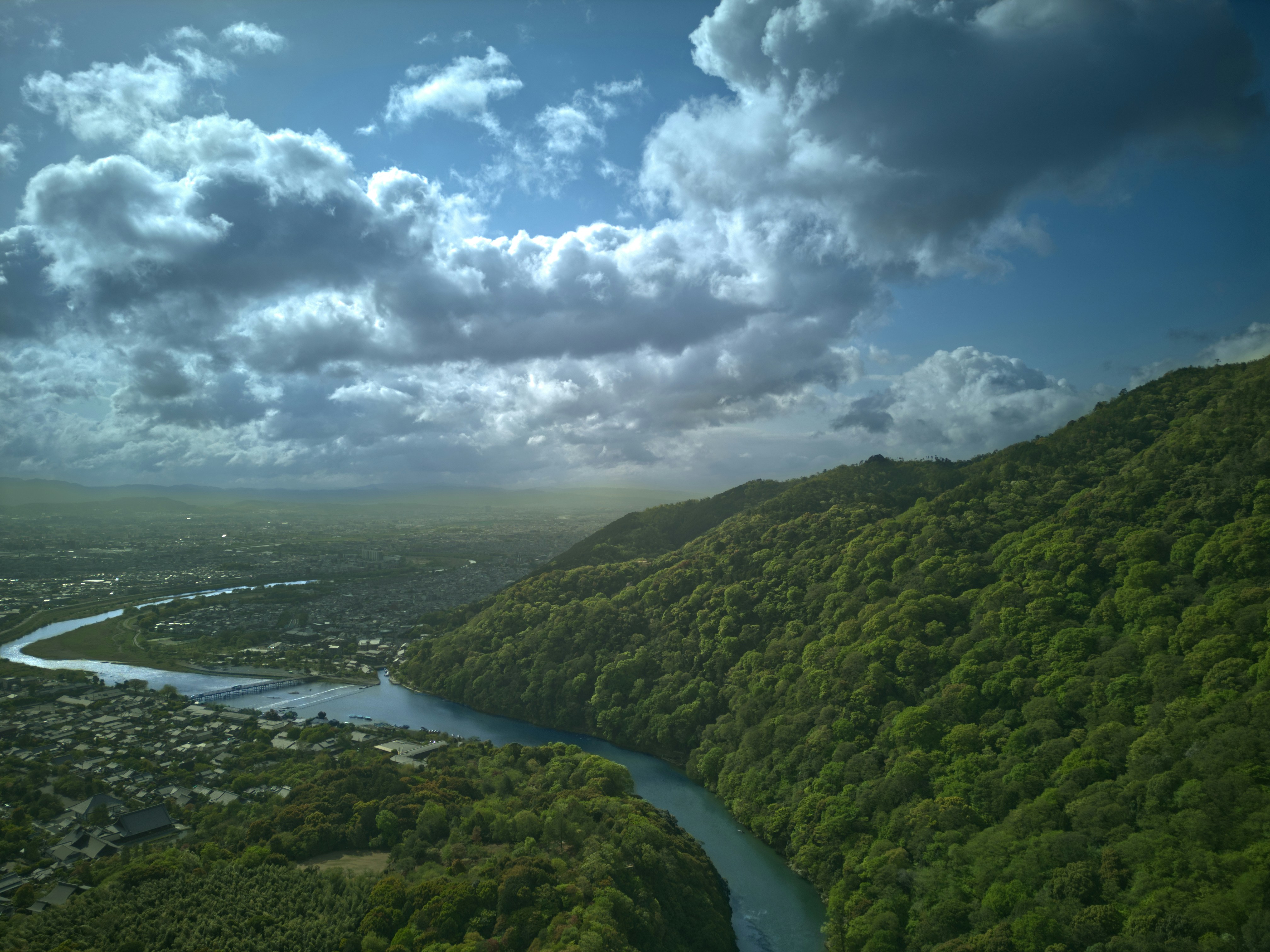 Lush green hills with a winding river under a sky filled with dramatic clouds.