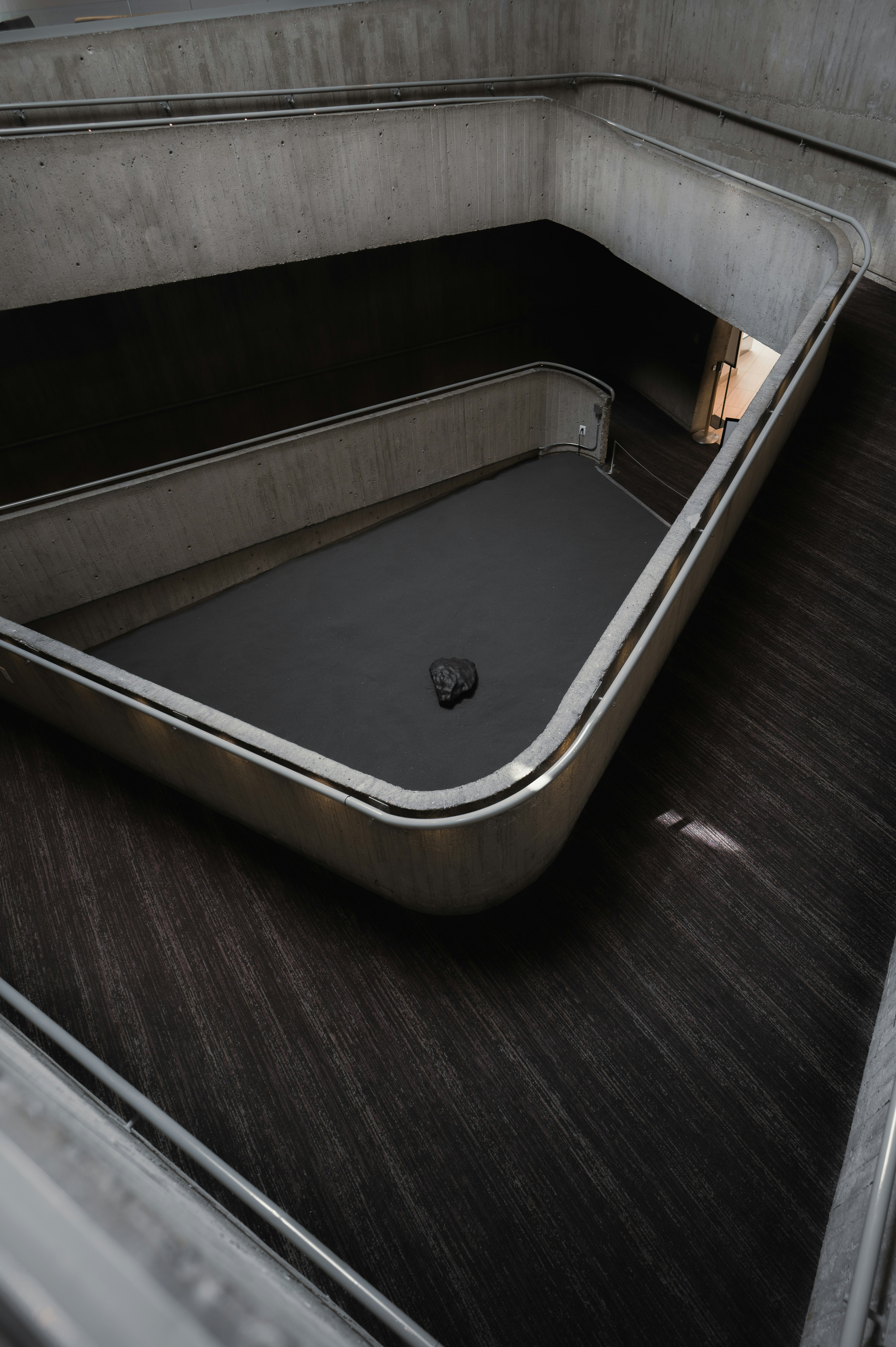 Descent by Design: A lone rock anchors a quiet concrete atrium