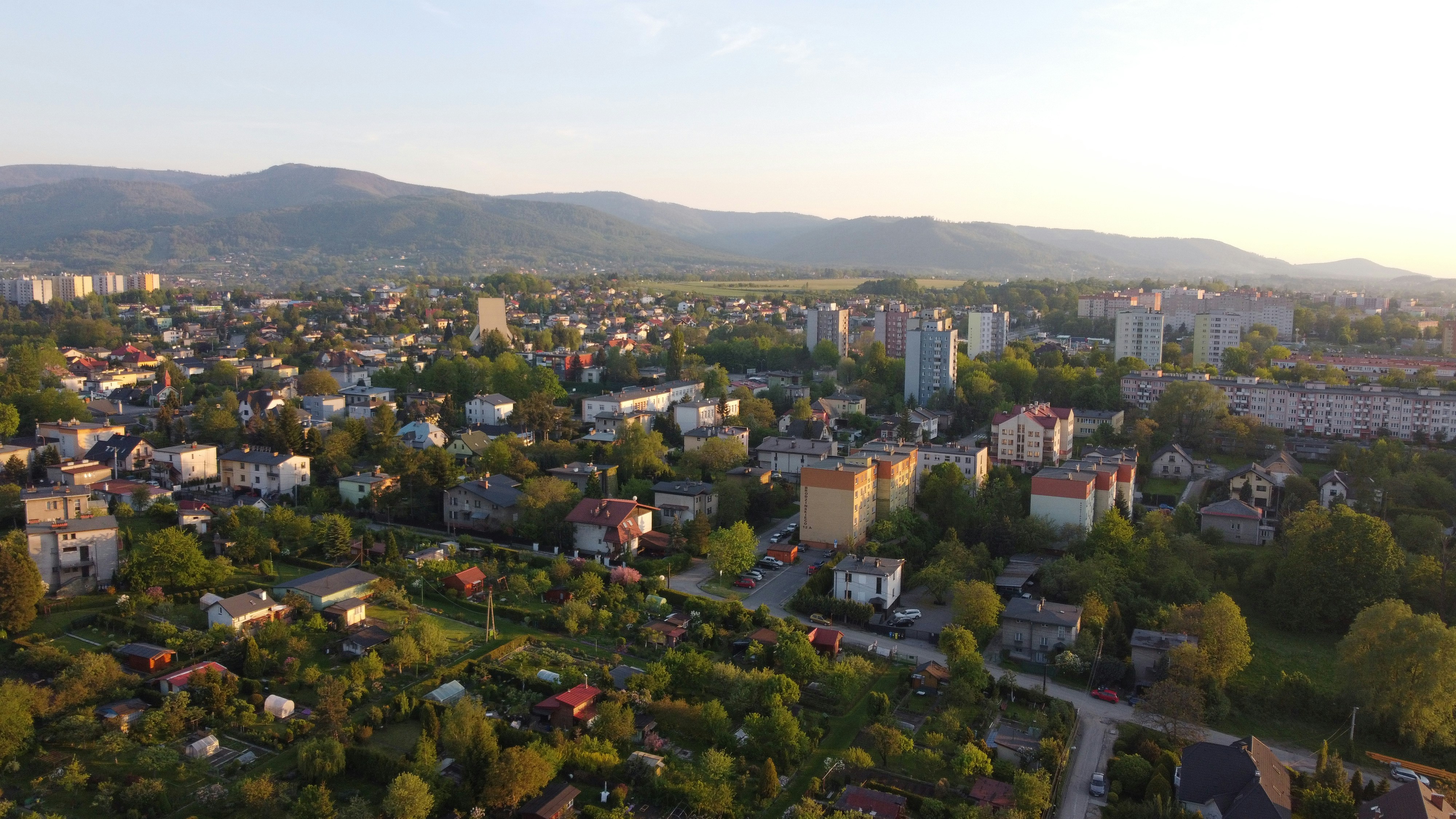Aerial view of a cityscape with lush greenery and distant mountains under a clear sky.