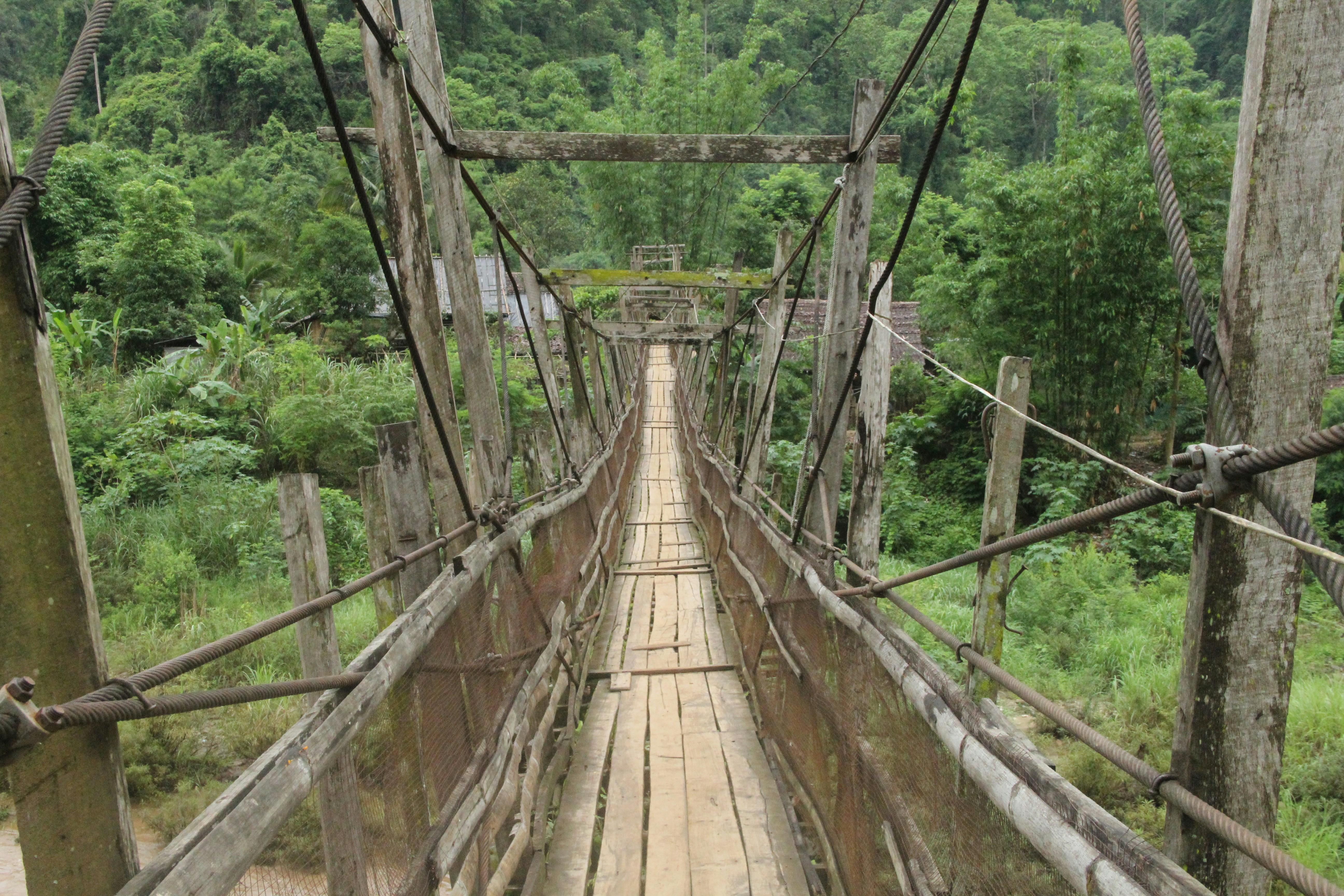 Suspension bridge made of weathered wood stretches over lush greenery, inviting adventure and exploration.