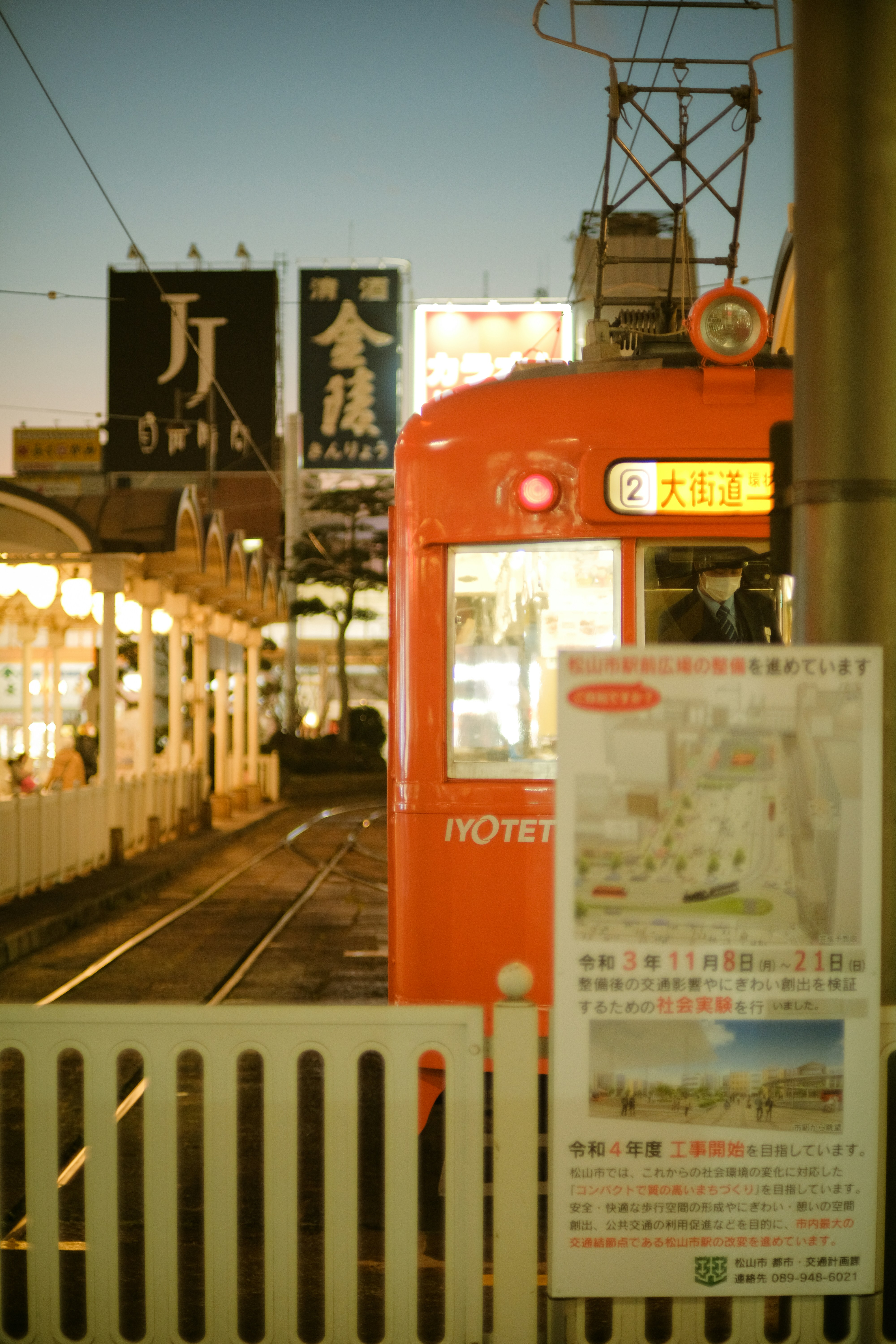 Crimson Streetcar Framed by Neon Signs at a Japanese Tram Platform