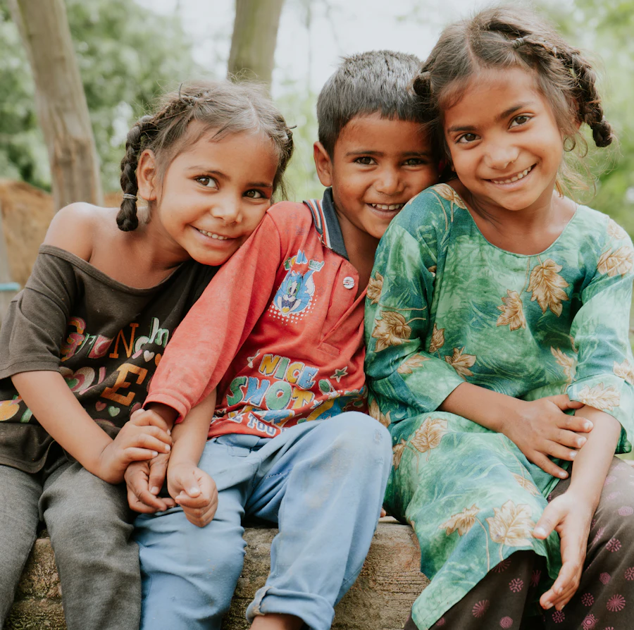 Three children smiling and sitting closely together, showcasing their friendship and playful spirit in a natural setting.