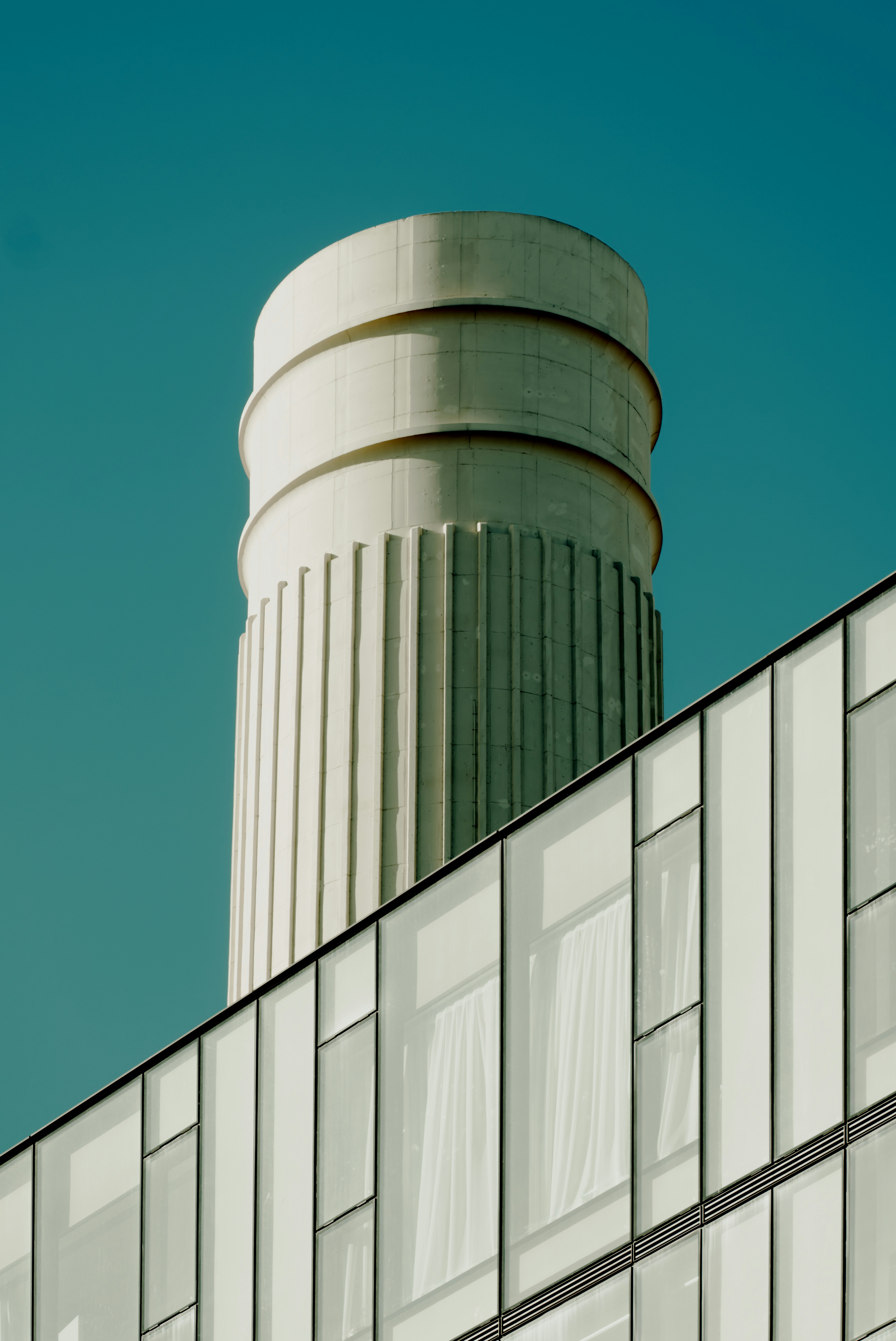 Teal Sky Over a Cylindrical Vent Tower Above a Glass Facade