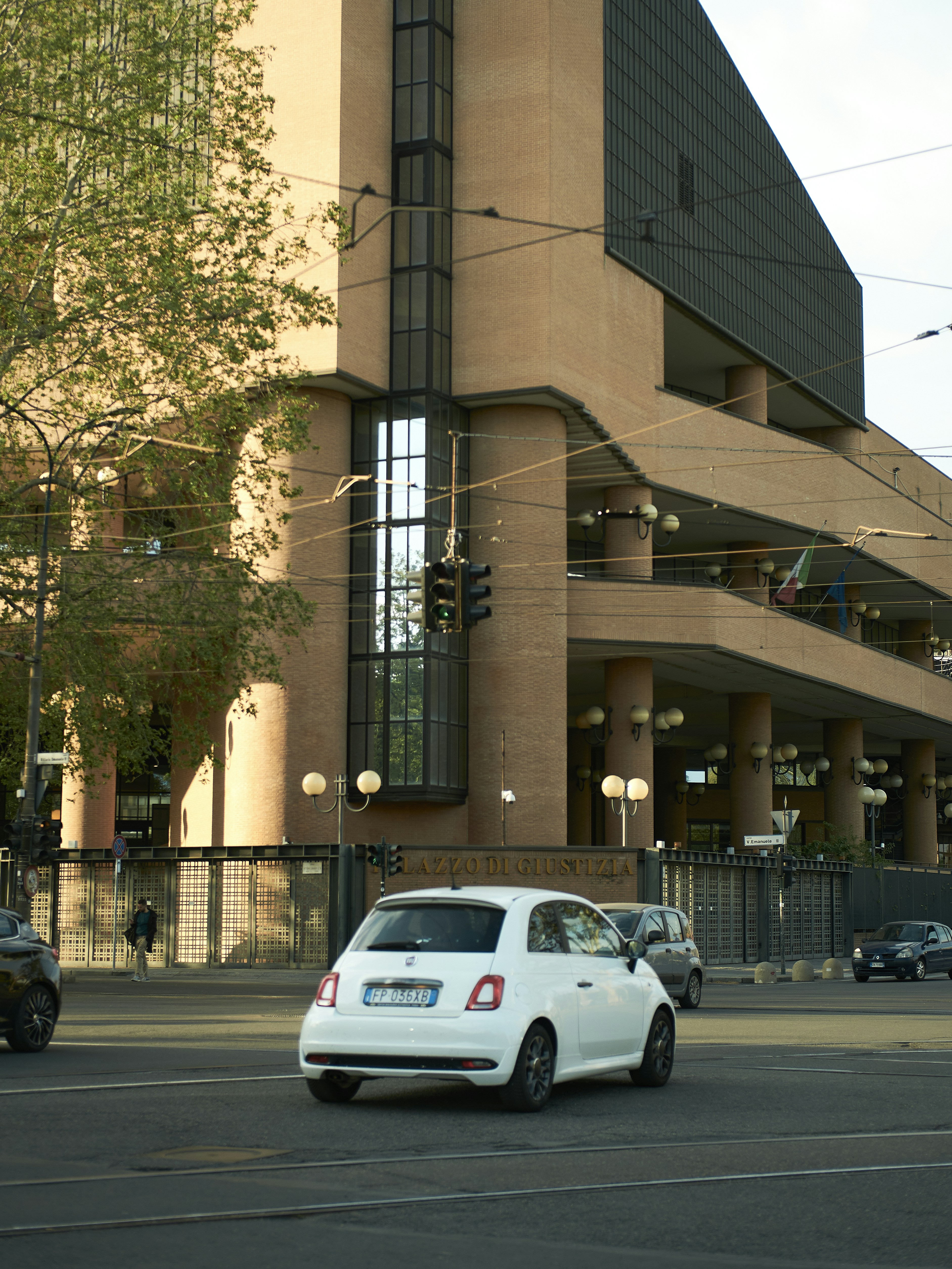 A white car driving down a street next to a tall building photo – Free ...
