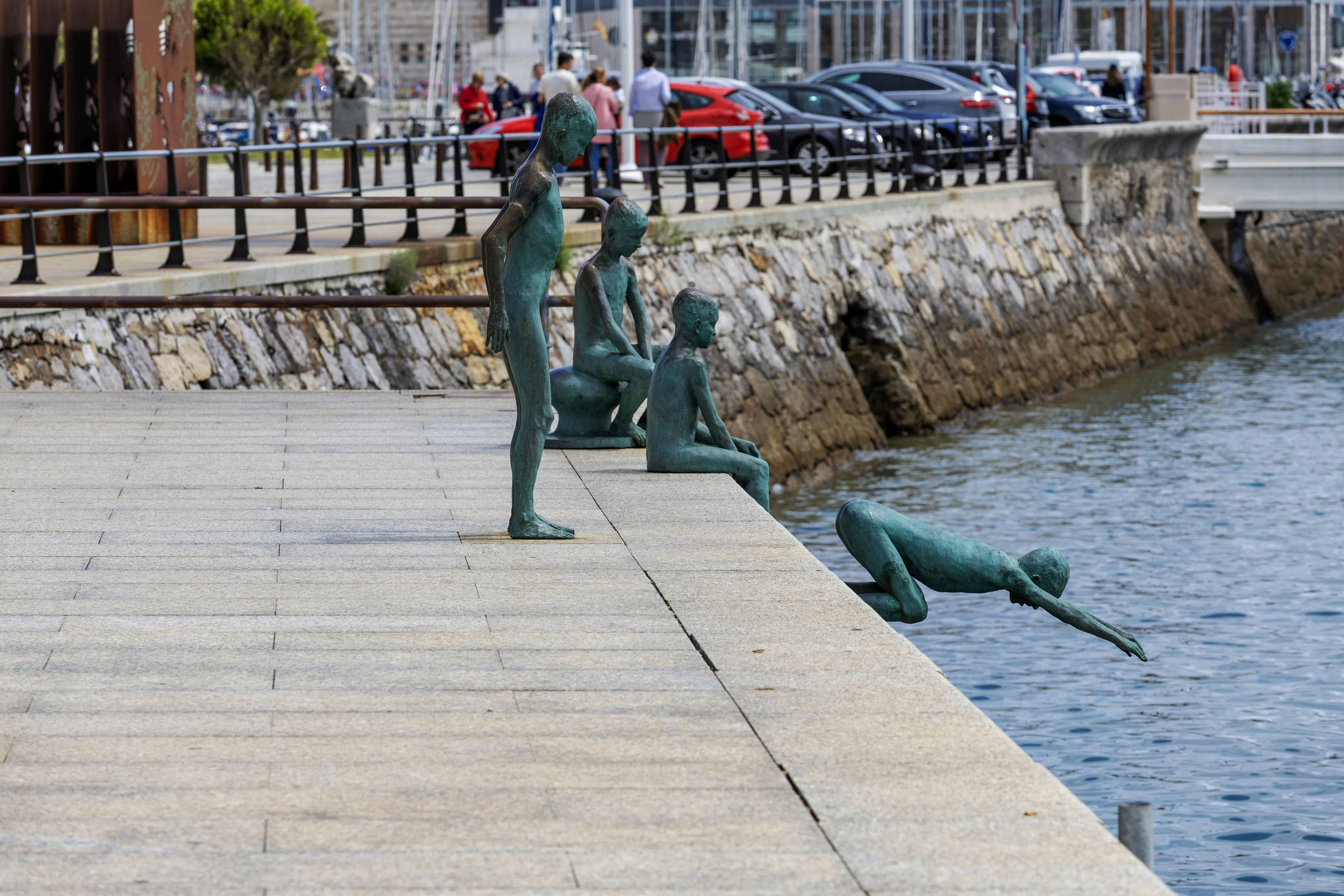 A statue of three people sitting on a dock next to a body of water ...