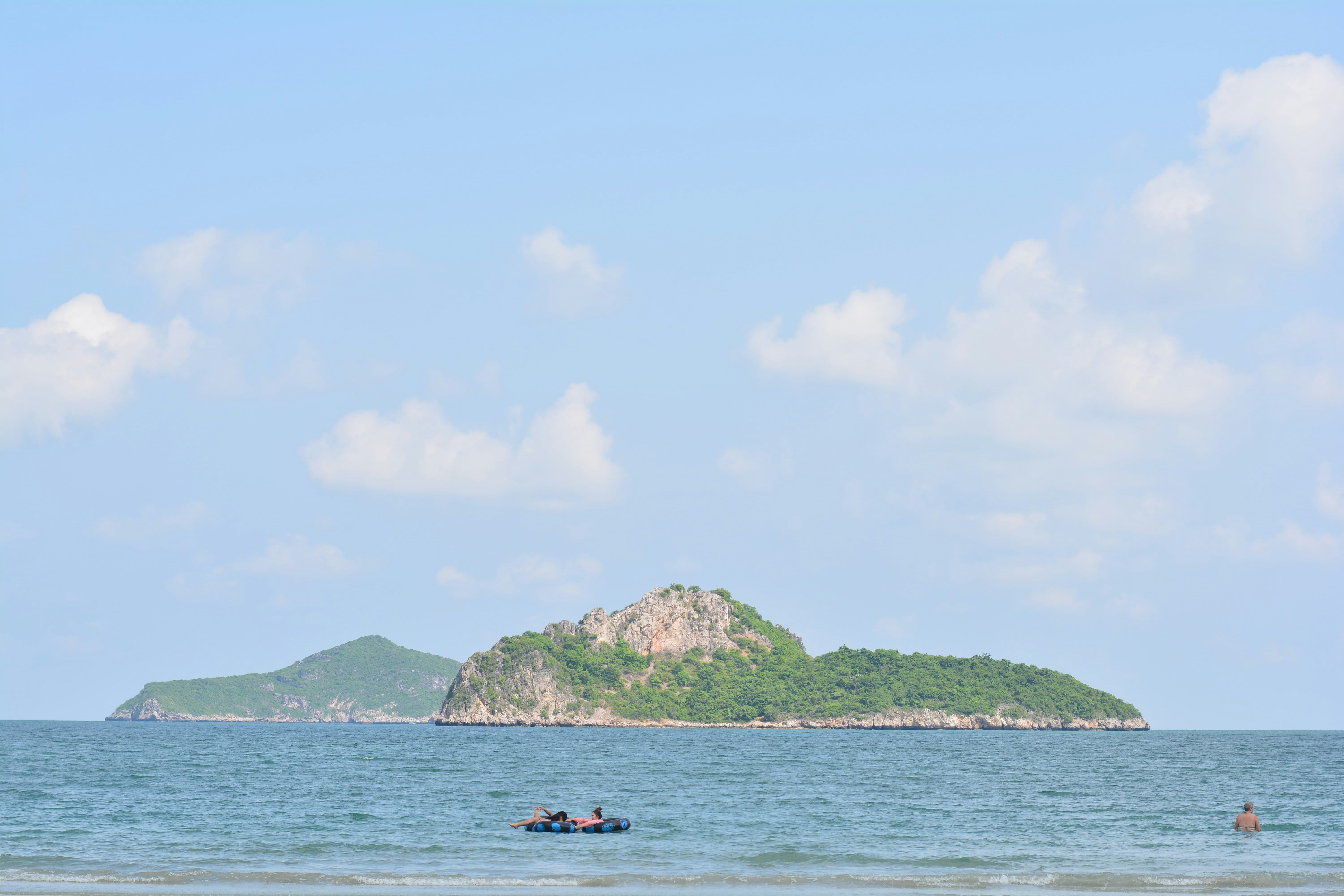 Distant island with rocky peak surrounded by calm blue sea under a partly cloudy sky.