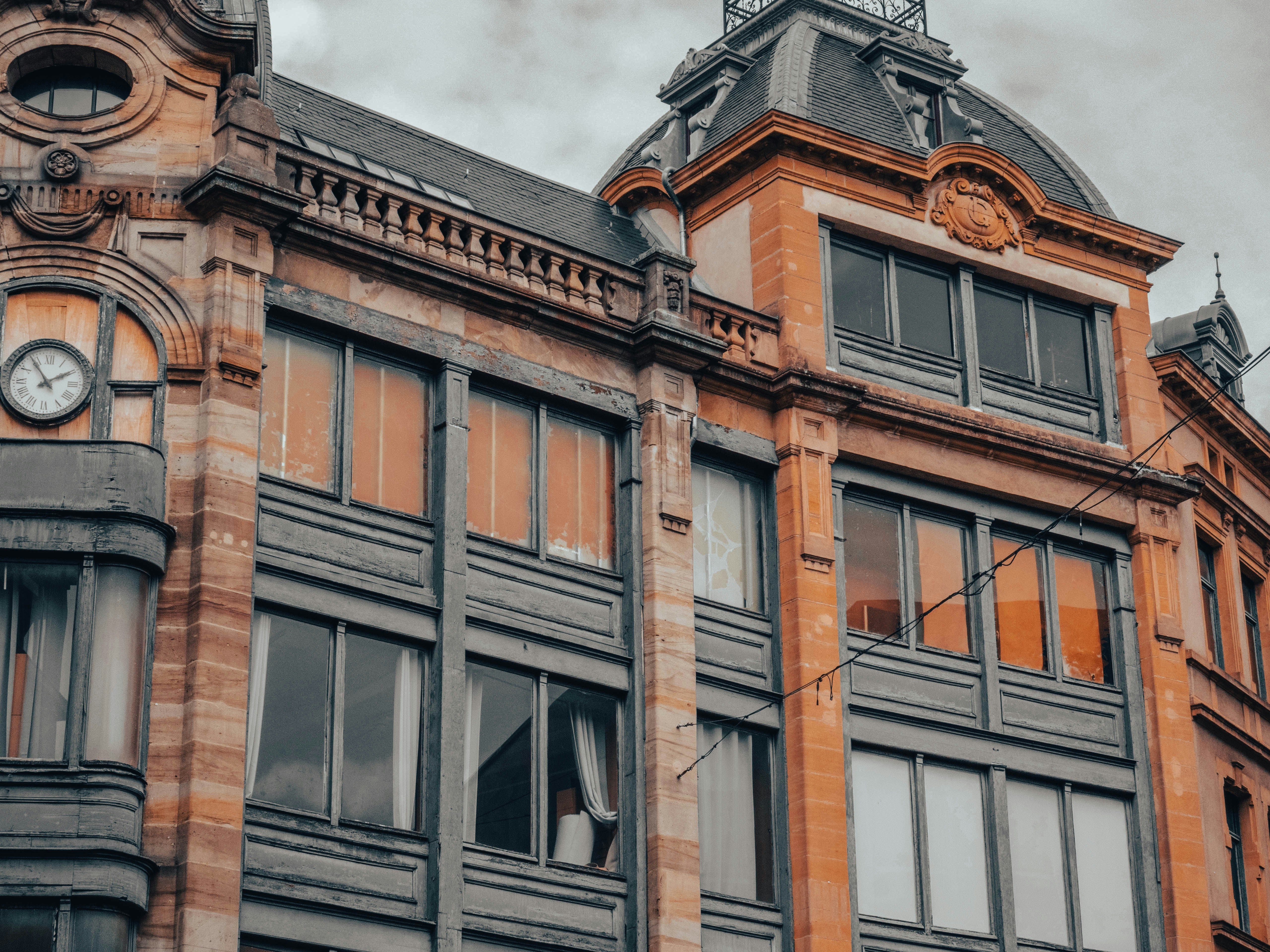 Historic building facade with ornate Victorian architecture and large modern windows under a cloudy sky.