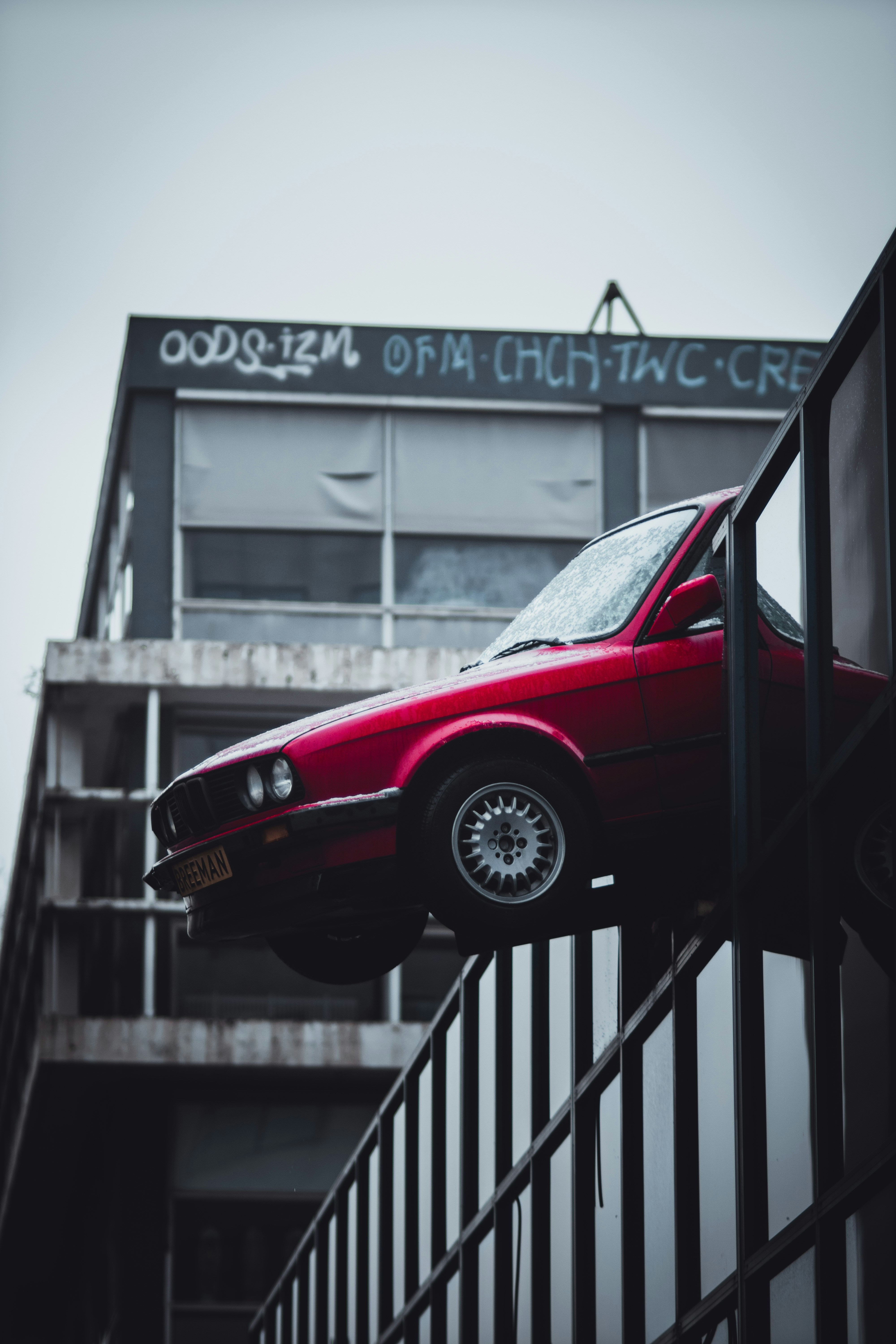 A red car precariously positioned on the edge of a modern building, showcasing urban creativity and architectural boldness.