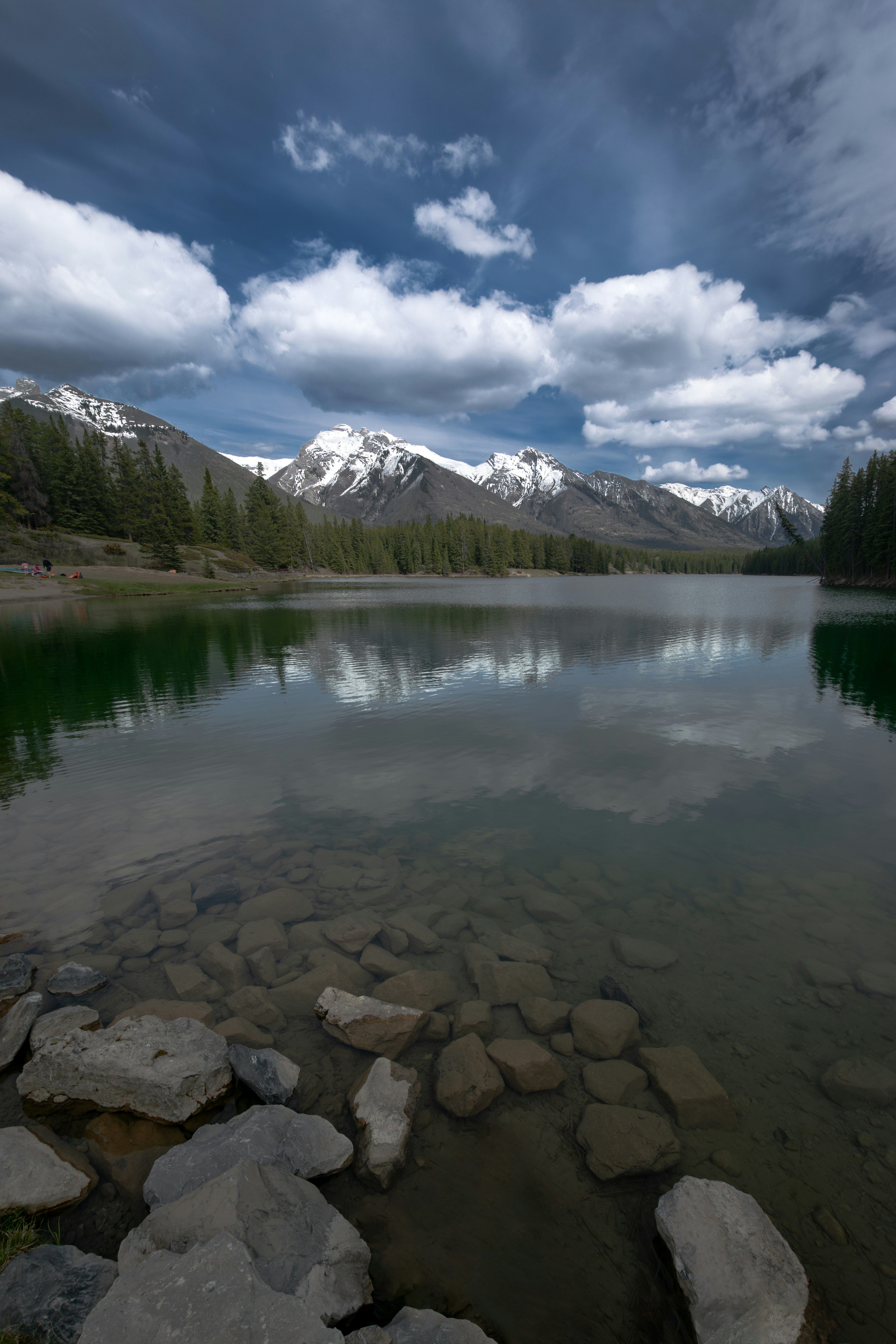 View of Johnson Lake with reflection of the mountains on it on a blue sky with clouds day. Banff National Park, Canada, Jun/22.