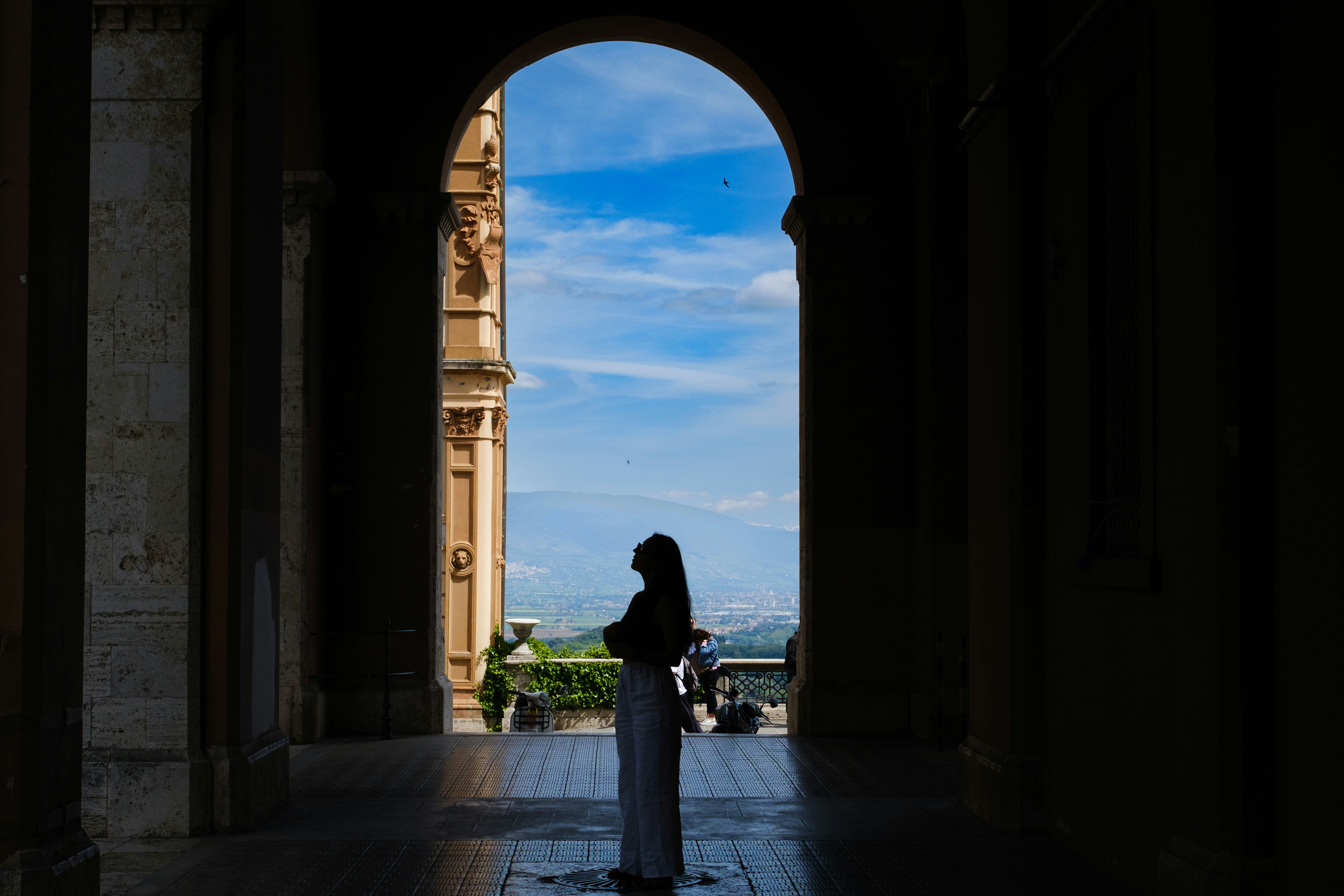 A woman standing in an archway with a view of a city photo – Free Arch ...