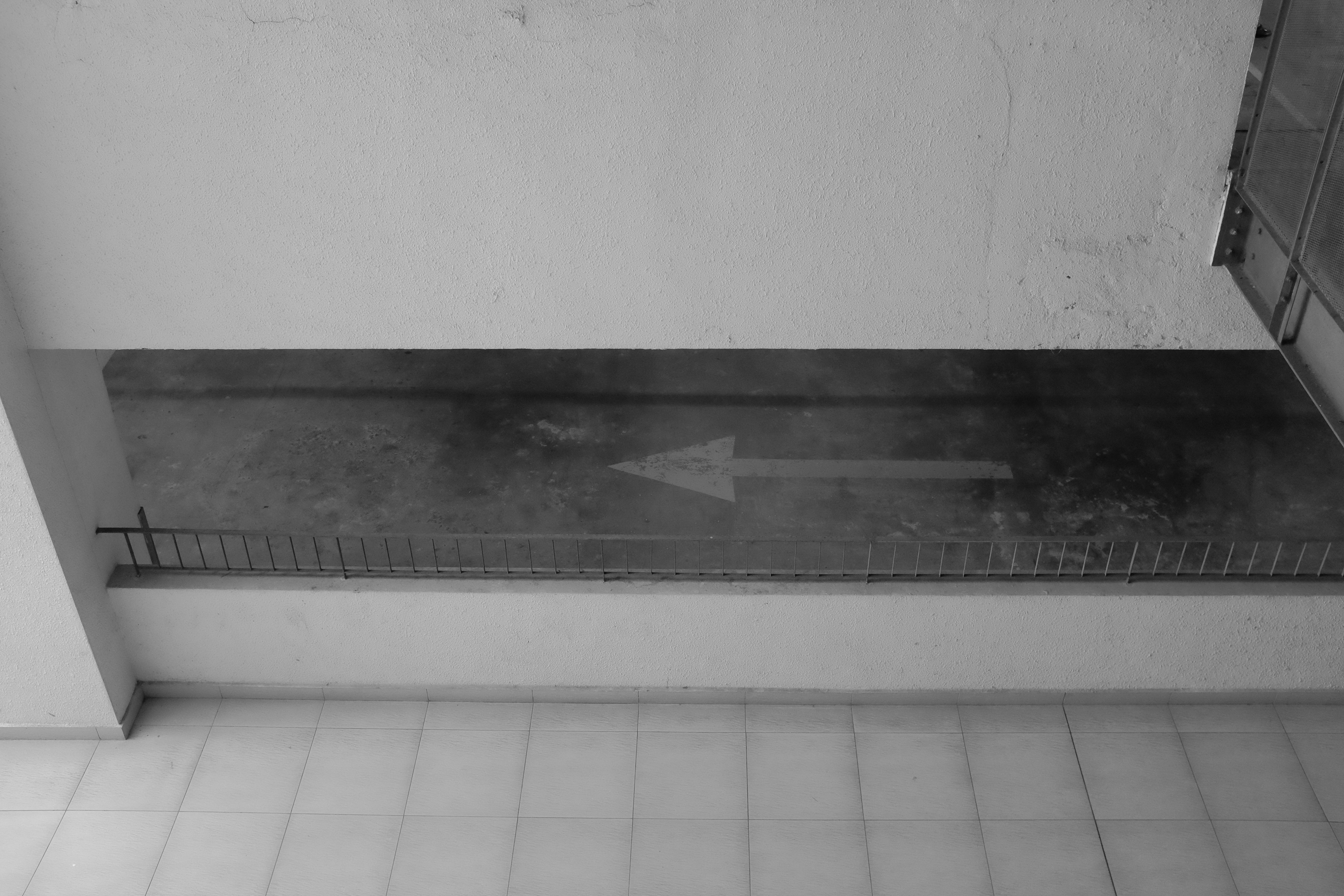Black and white photograph of an arrow painted on a weathered concrete floor, framed by stark architectural lines.