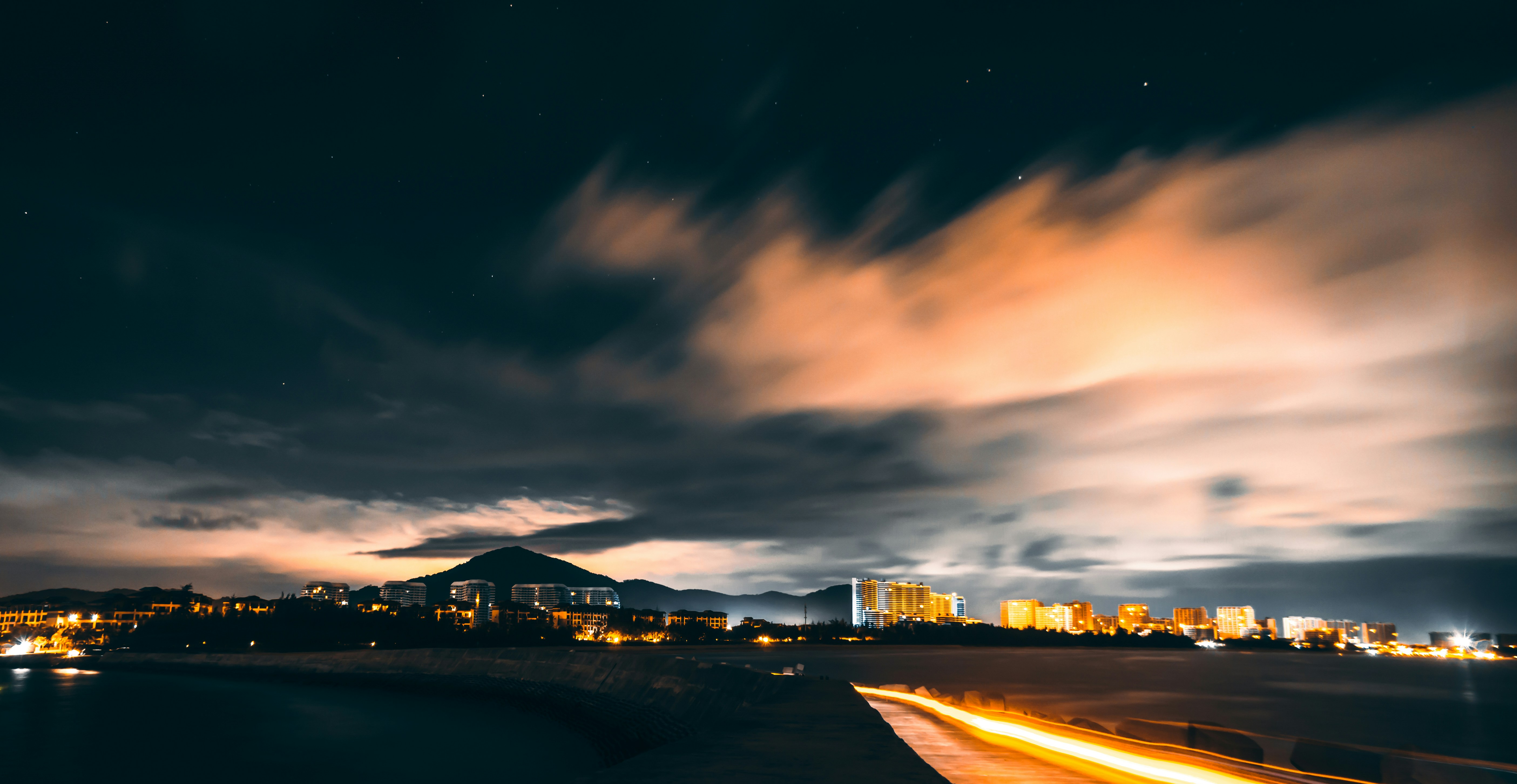 Long exposure of city skyline under swirling clouds and starry sky.