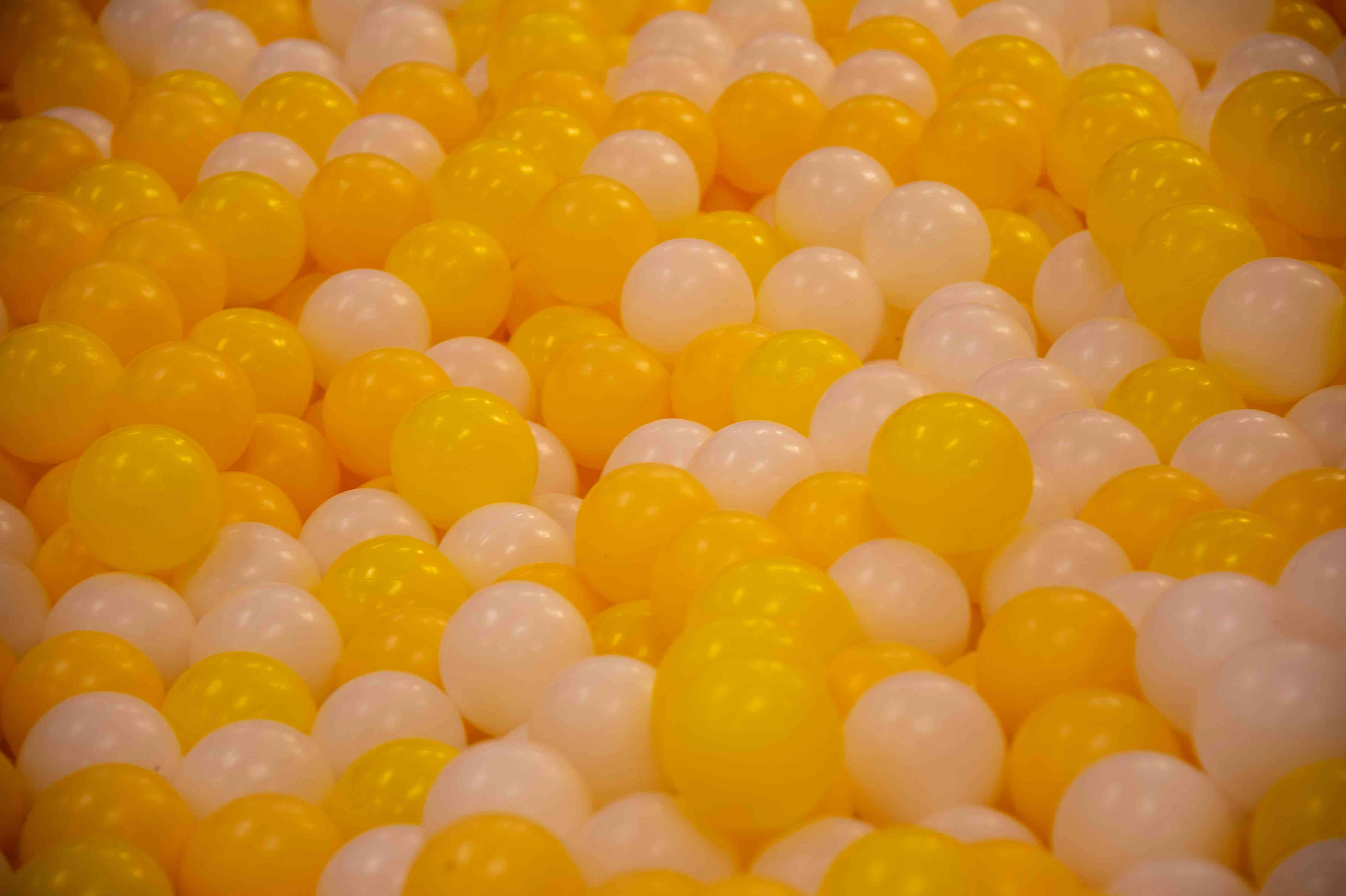 Colorful arrangement of yellow and white plastic balls creating a vibrant play area. The texture and colors invite playful interaction.