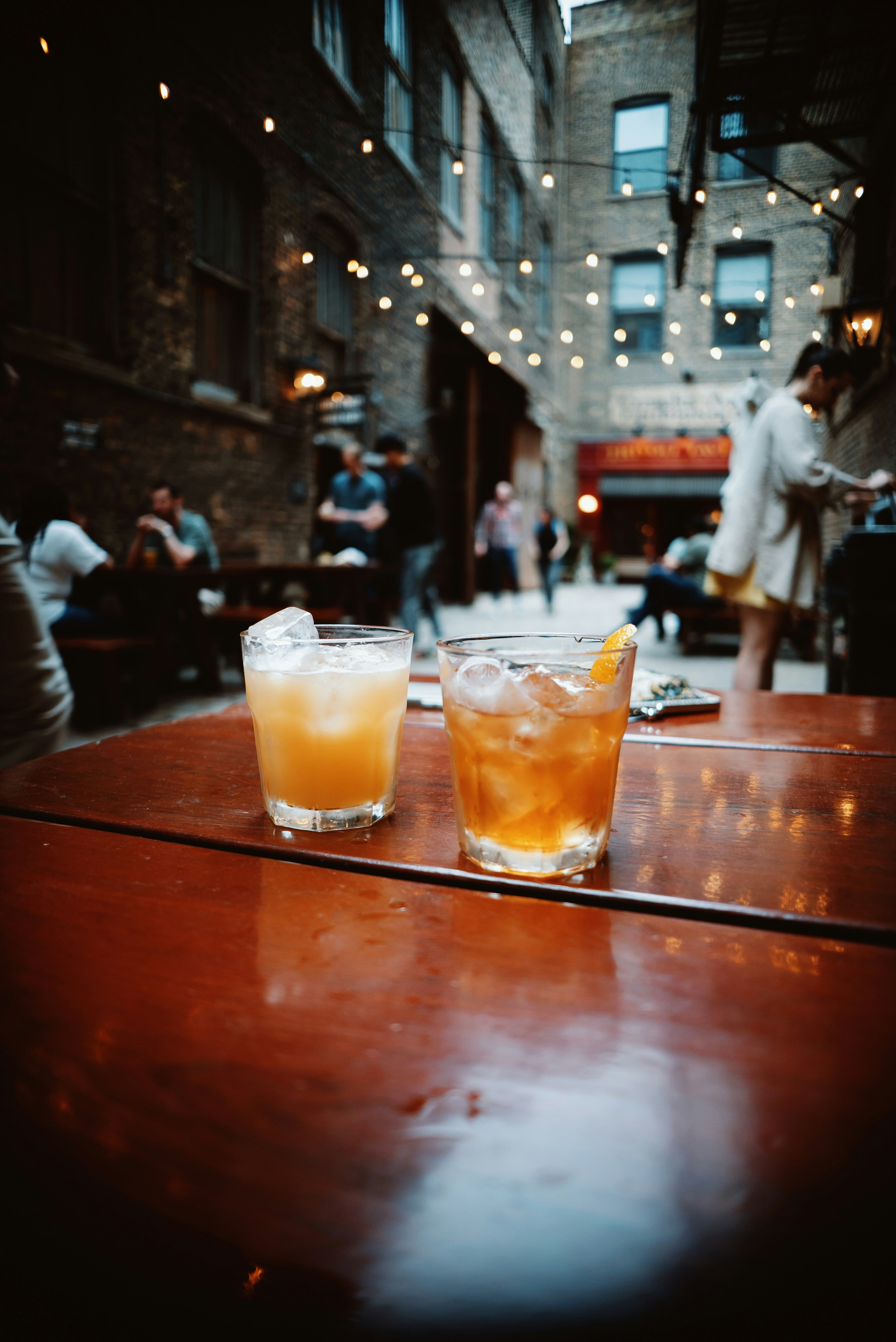 Two Iced Drinks on a Brick Courtyard Table Beneath Warm String Lights