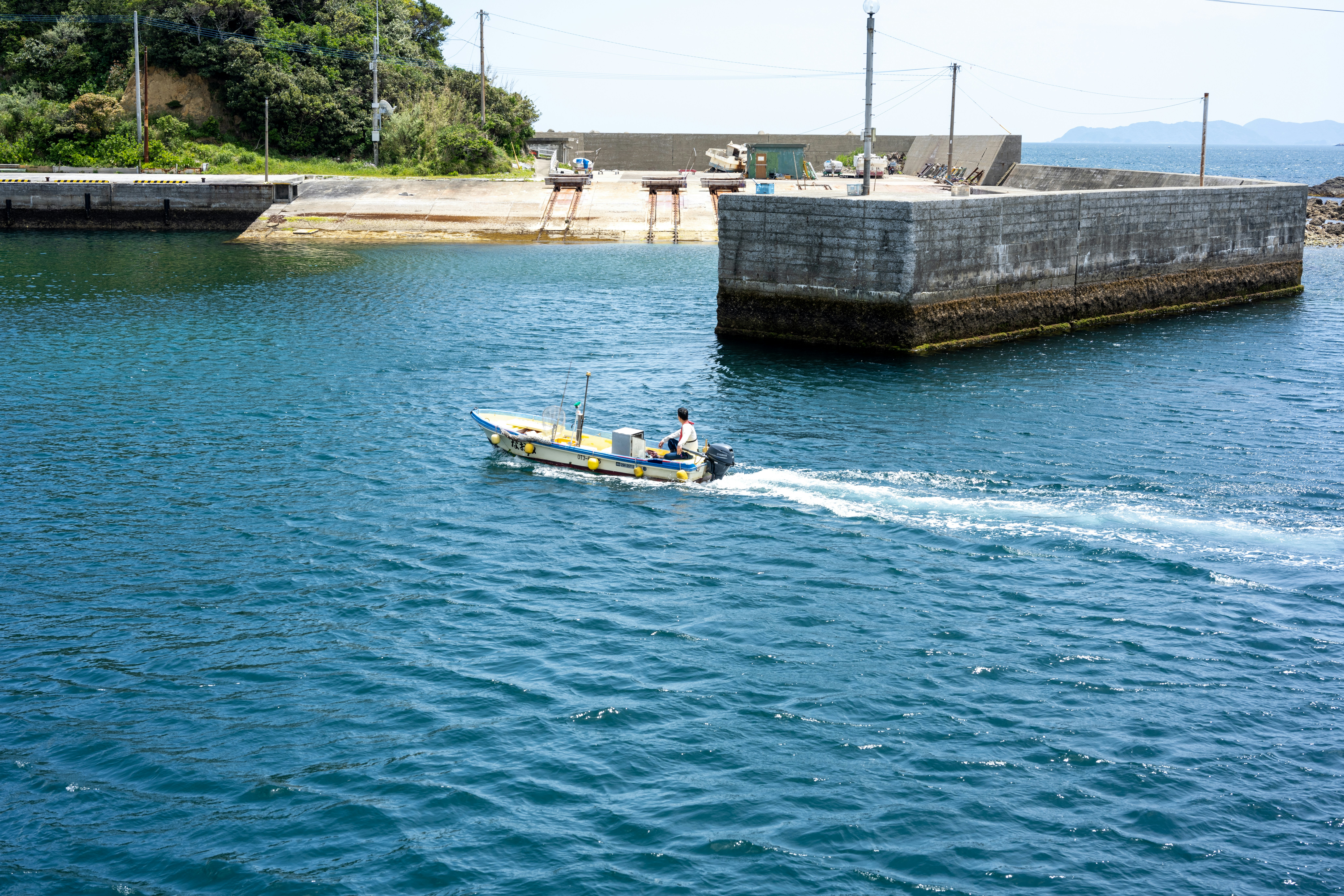 Turquoise Wake: A solitary motorboat threads the harbor past a weathered breakwater