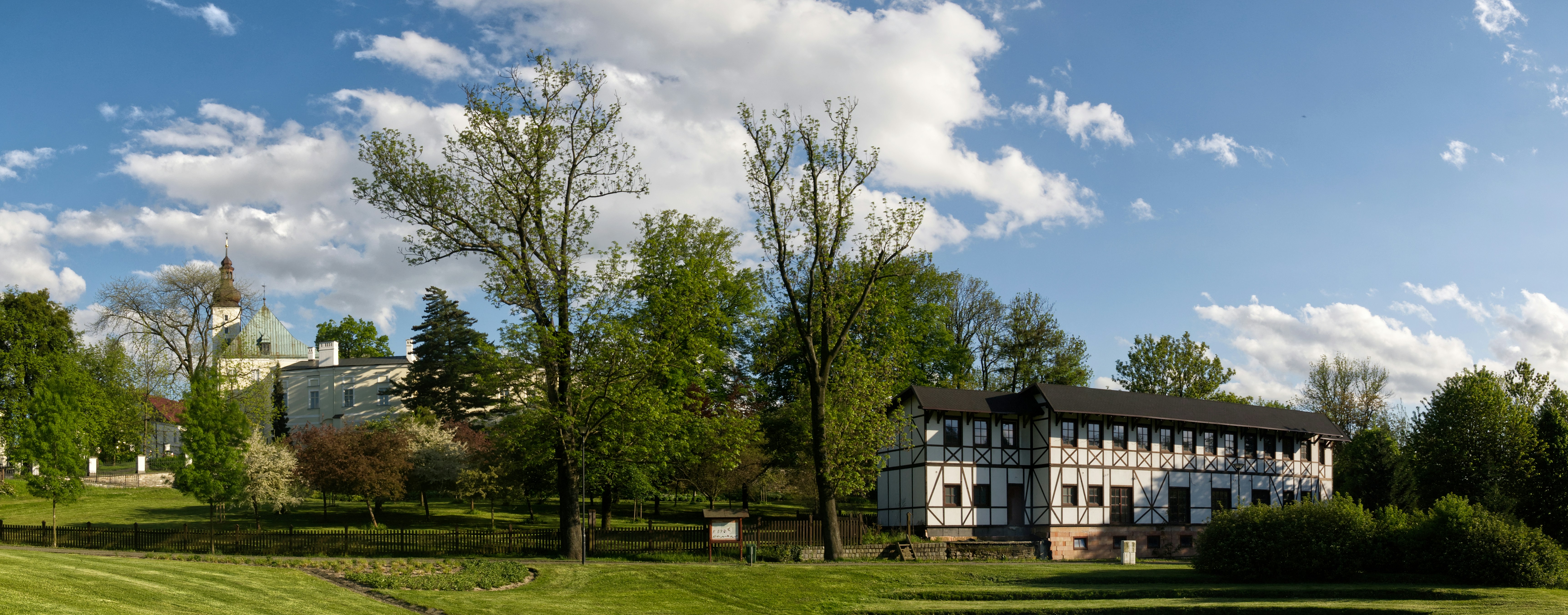 Historical building surrounded by lush greenery under a bright blue sky with scattered clouds.