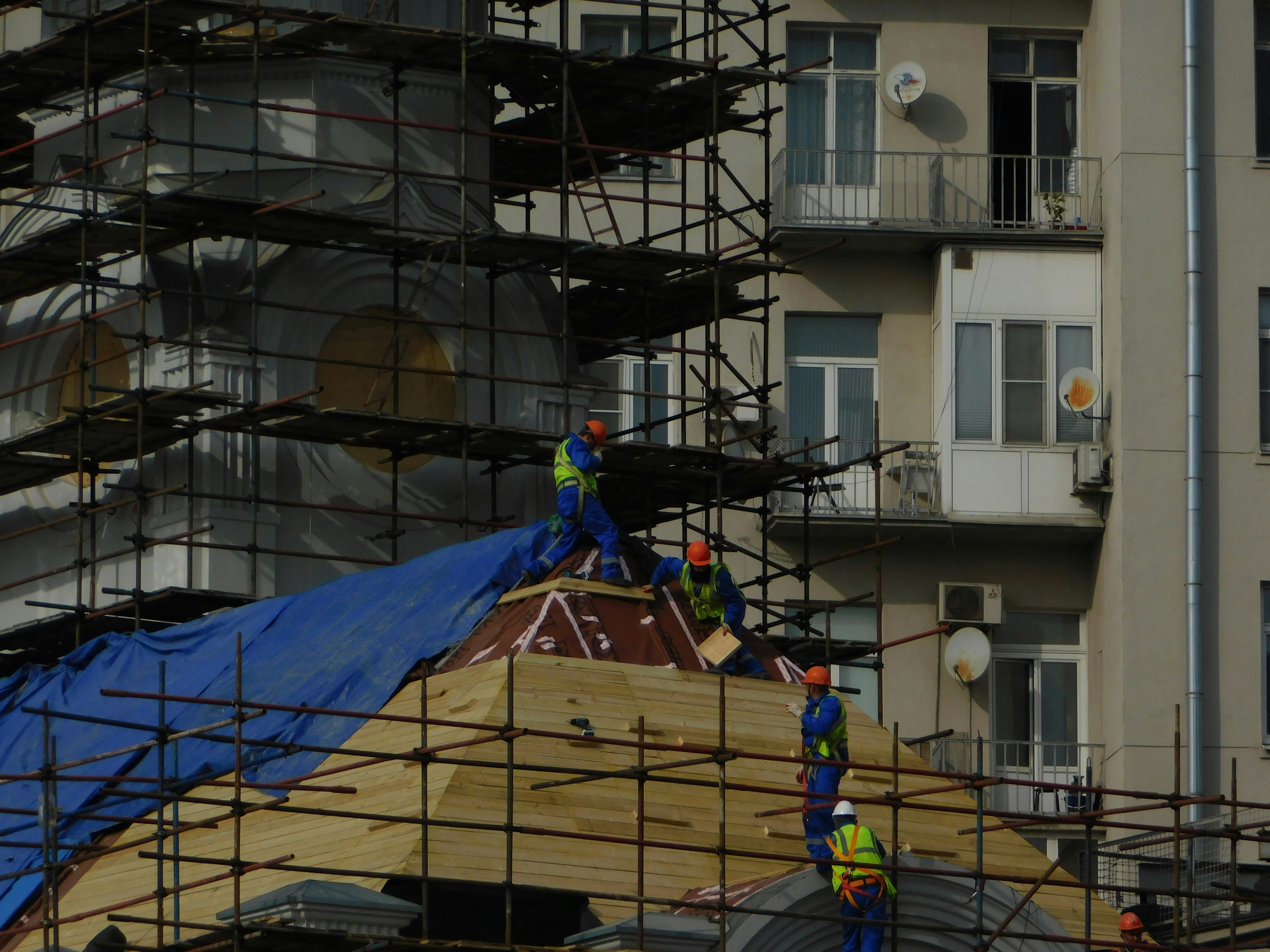 Crown of Timber and Steel: Builders Traverse a Curved Dome Shrouded in Blue Tarps