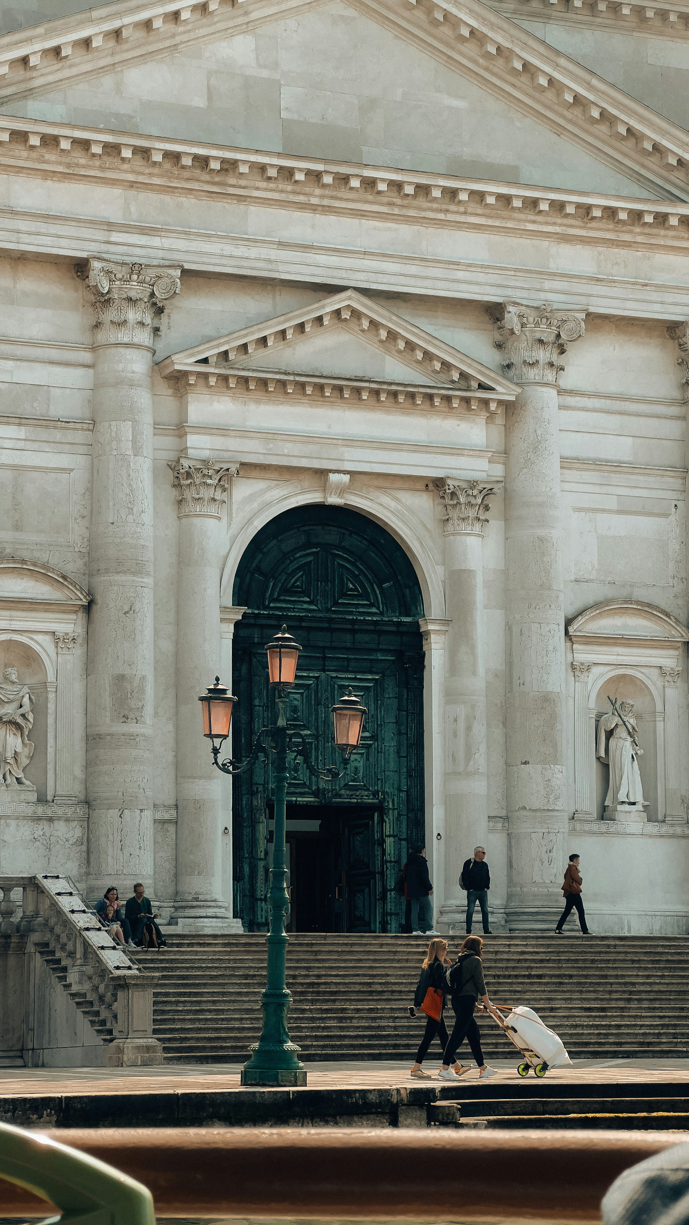 Stone Facade at the Steps: Lanterns, Pedestrians, and a Rolling Suitcase