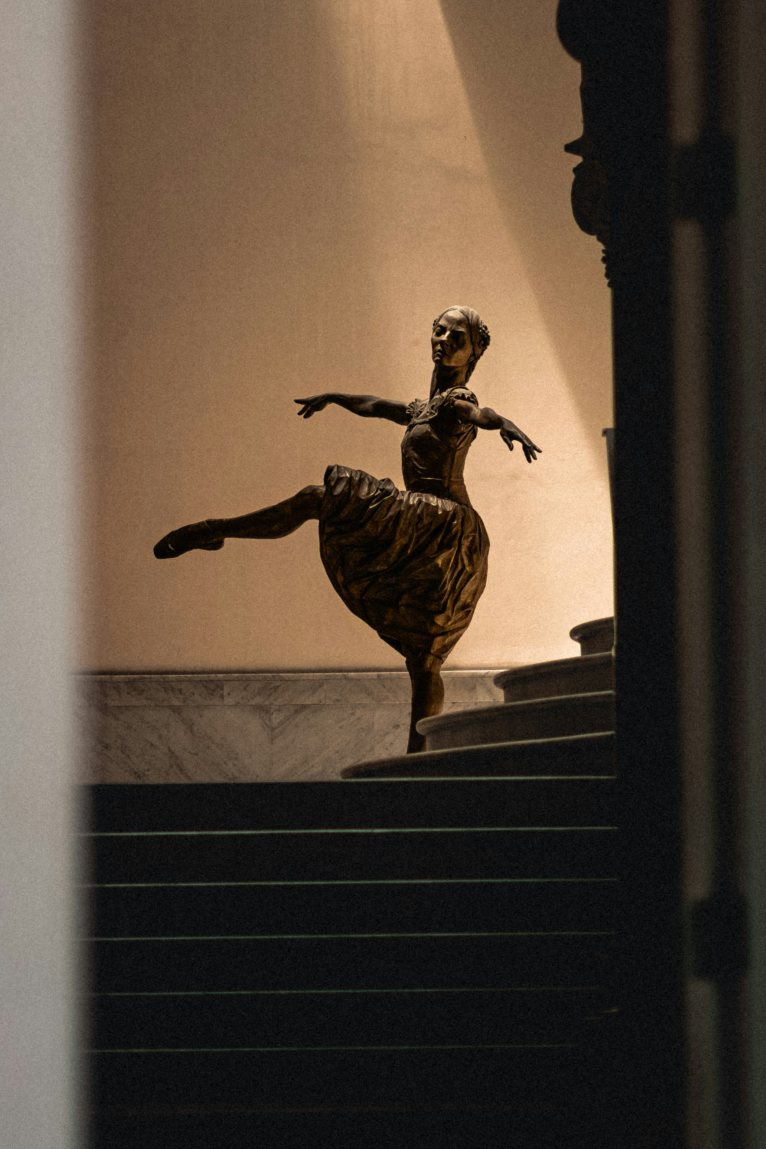 Silent Pirouette: Bronze Ballerina on a Warm-Backlit Staircase