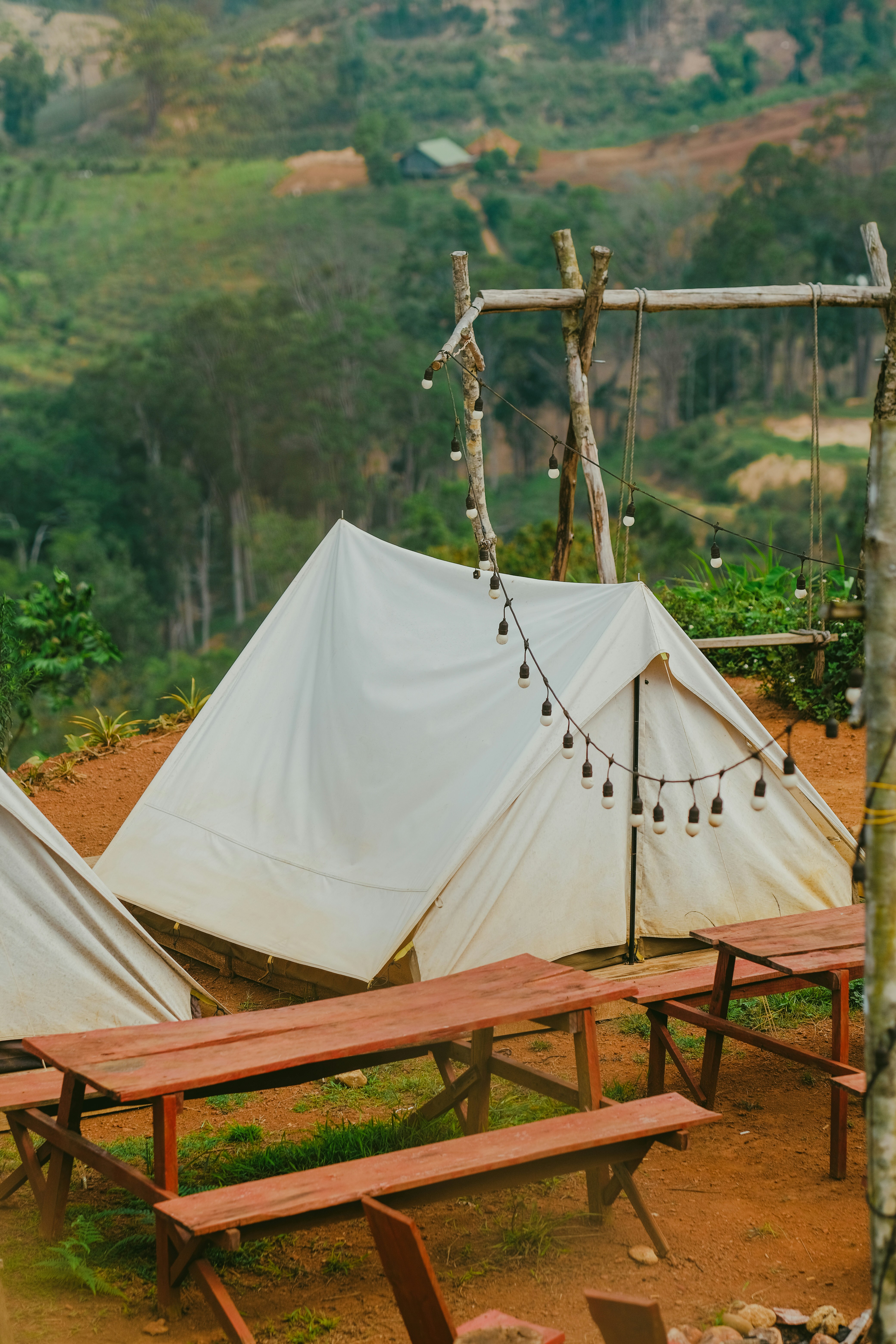 Lantern-Lit Camp on a Red-Dirt Terrace Beneath Verdant Hills