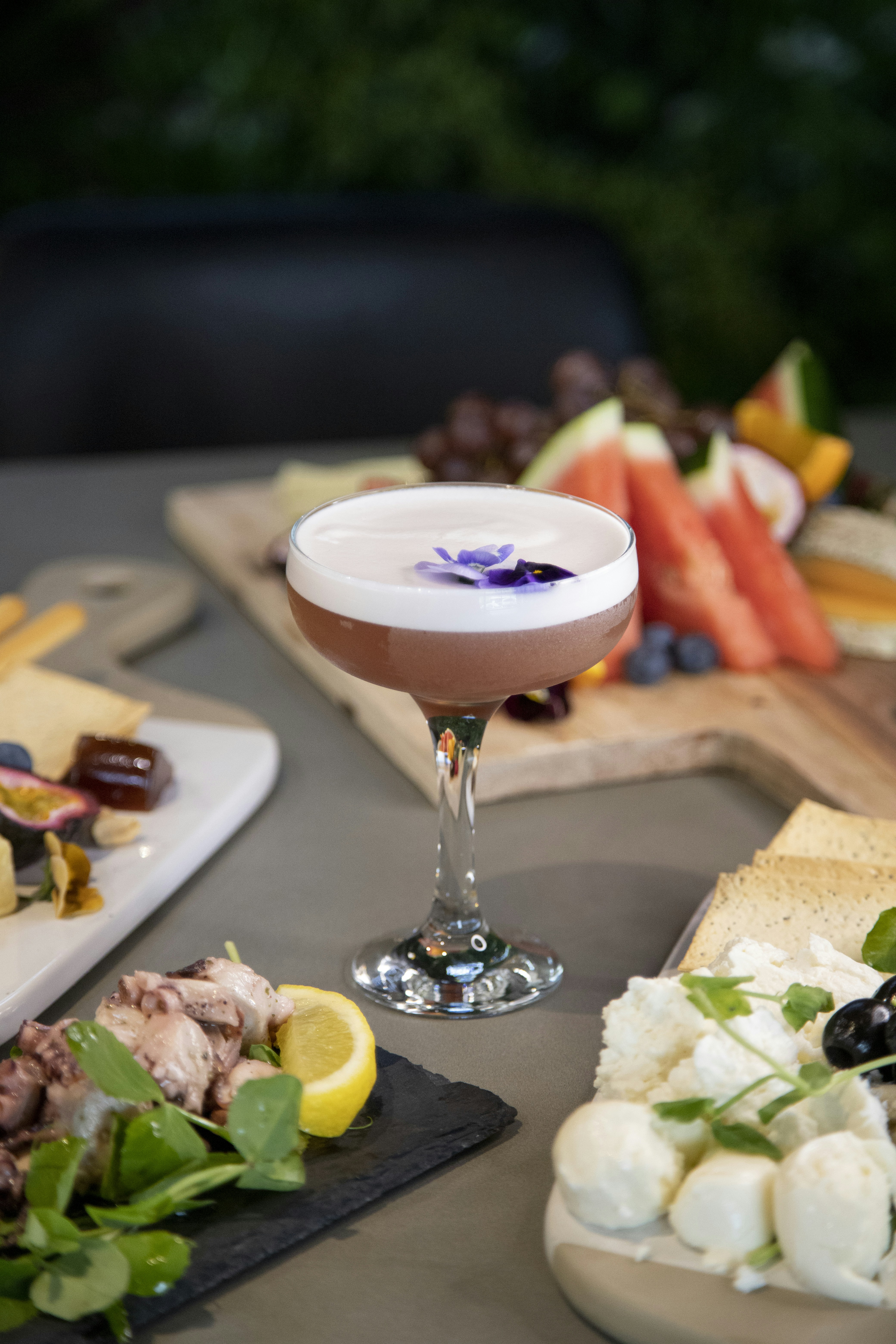 Cream-Topped Cocktail Framed by a Lush Charcuterie Spread
