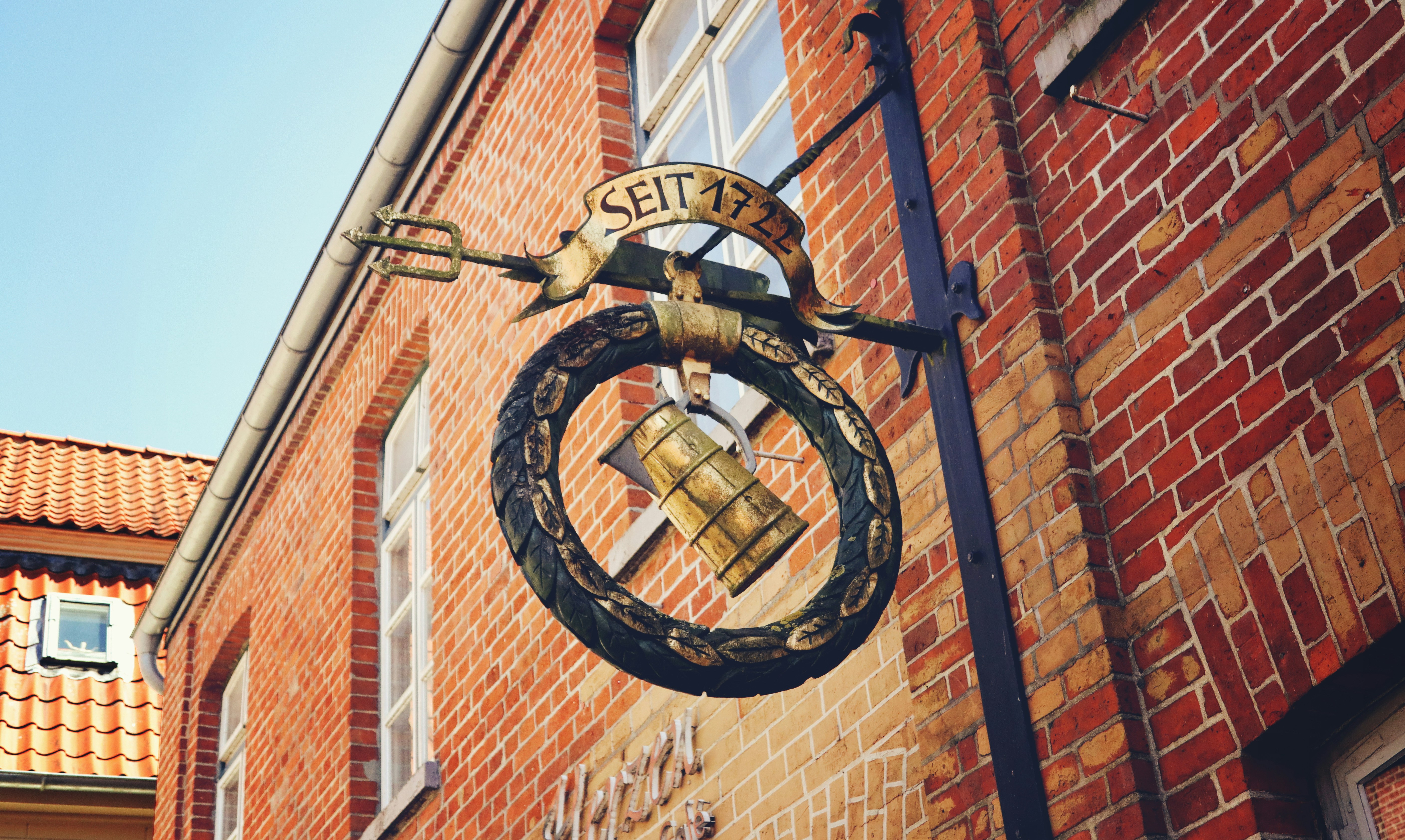 Ornate metallic serpent sign with a lantern and trident detail against historic brick buildings.