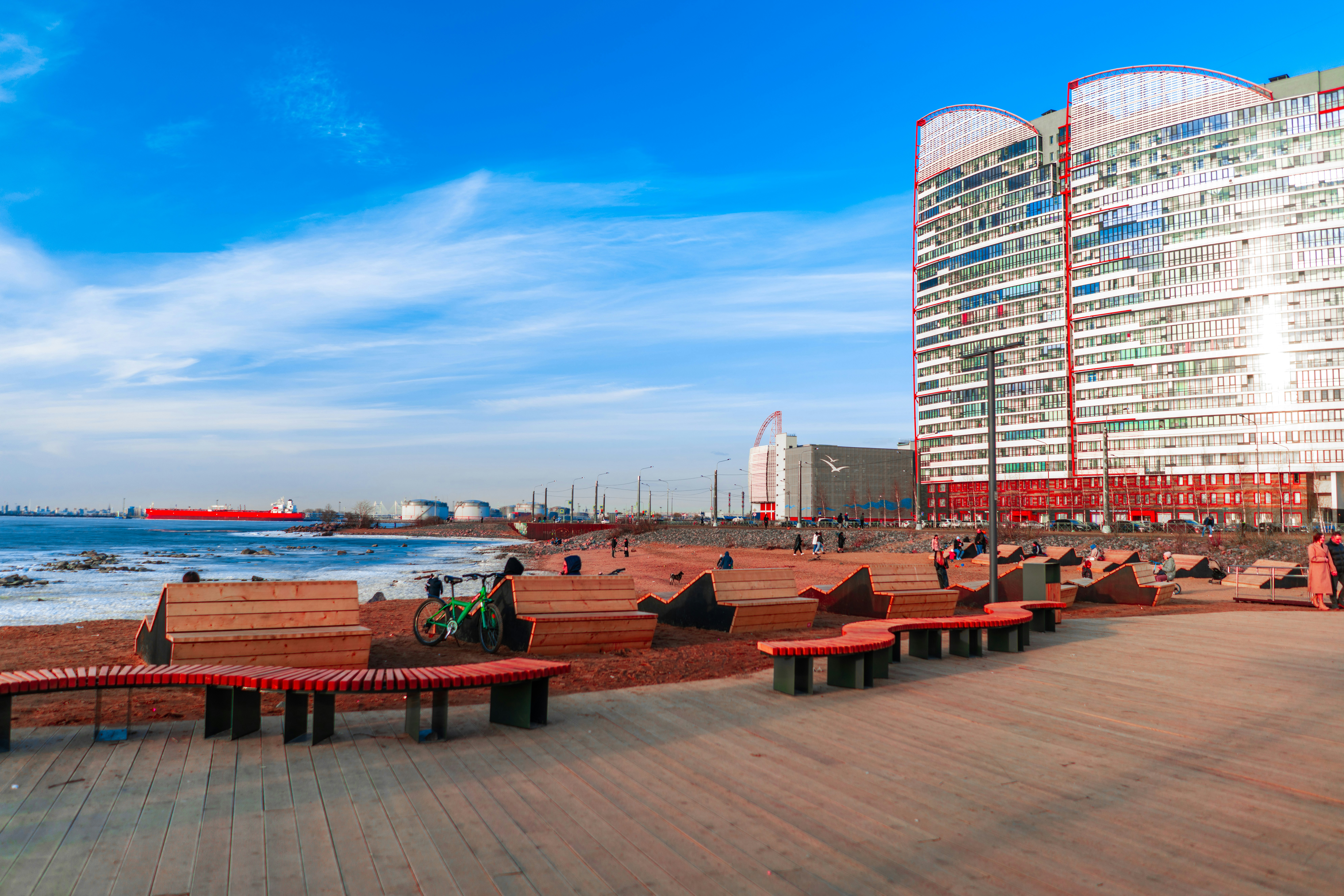 Sunlit Seafront Promenade: Red Loungers, Blue Sky, and a Glass-Walled Skyline