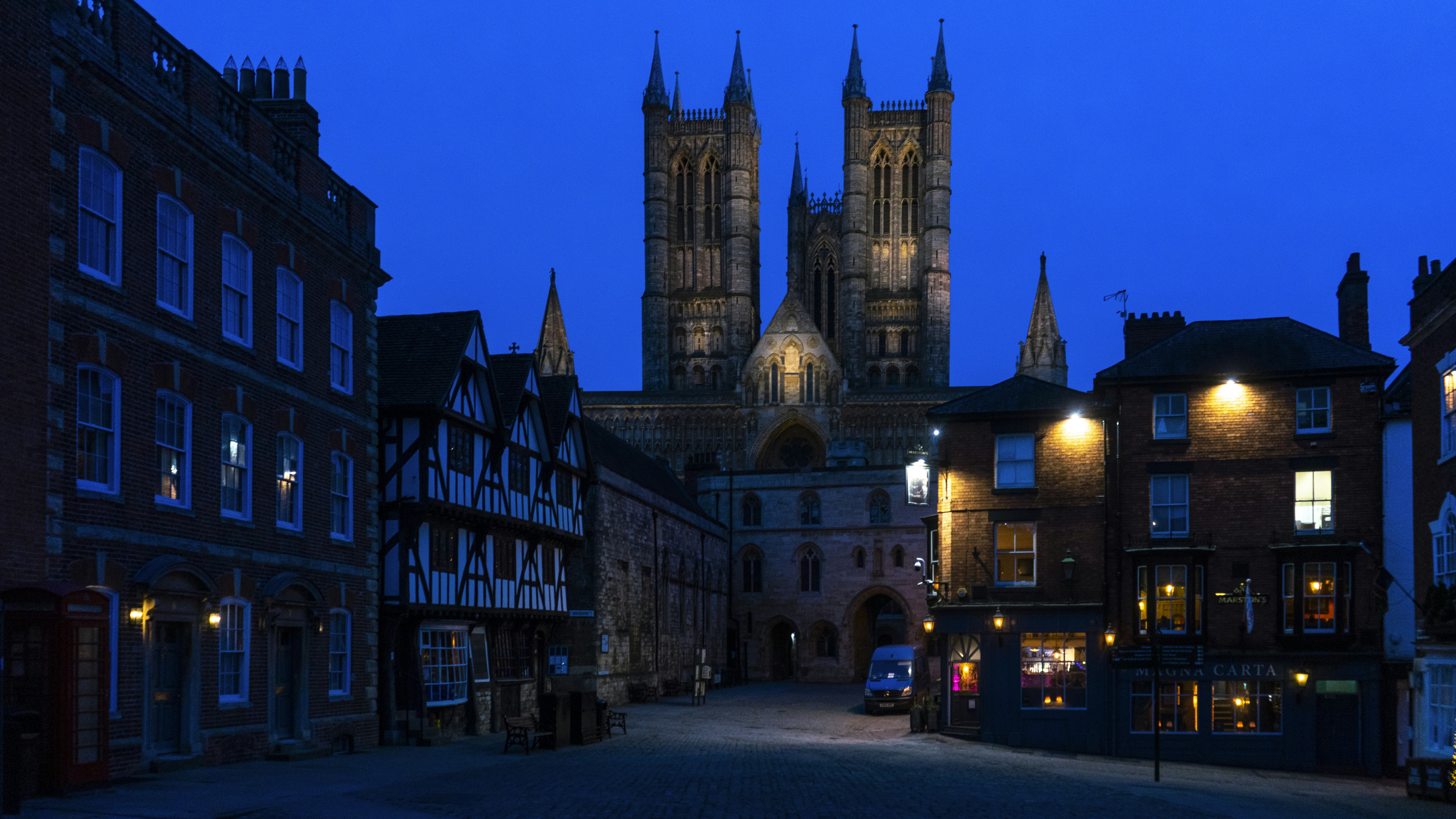 City street illuminated by warm lights against a majestic cathedral backdrop under a deep blue evening sky.