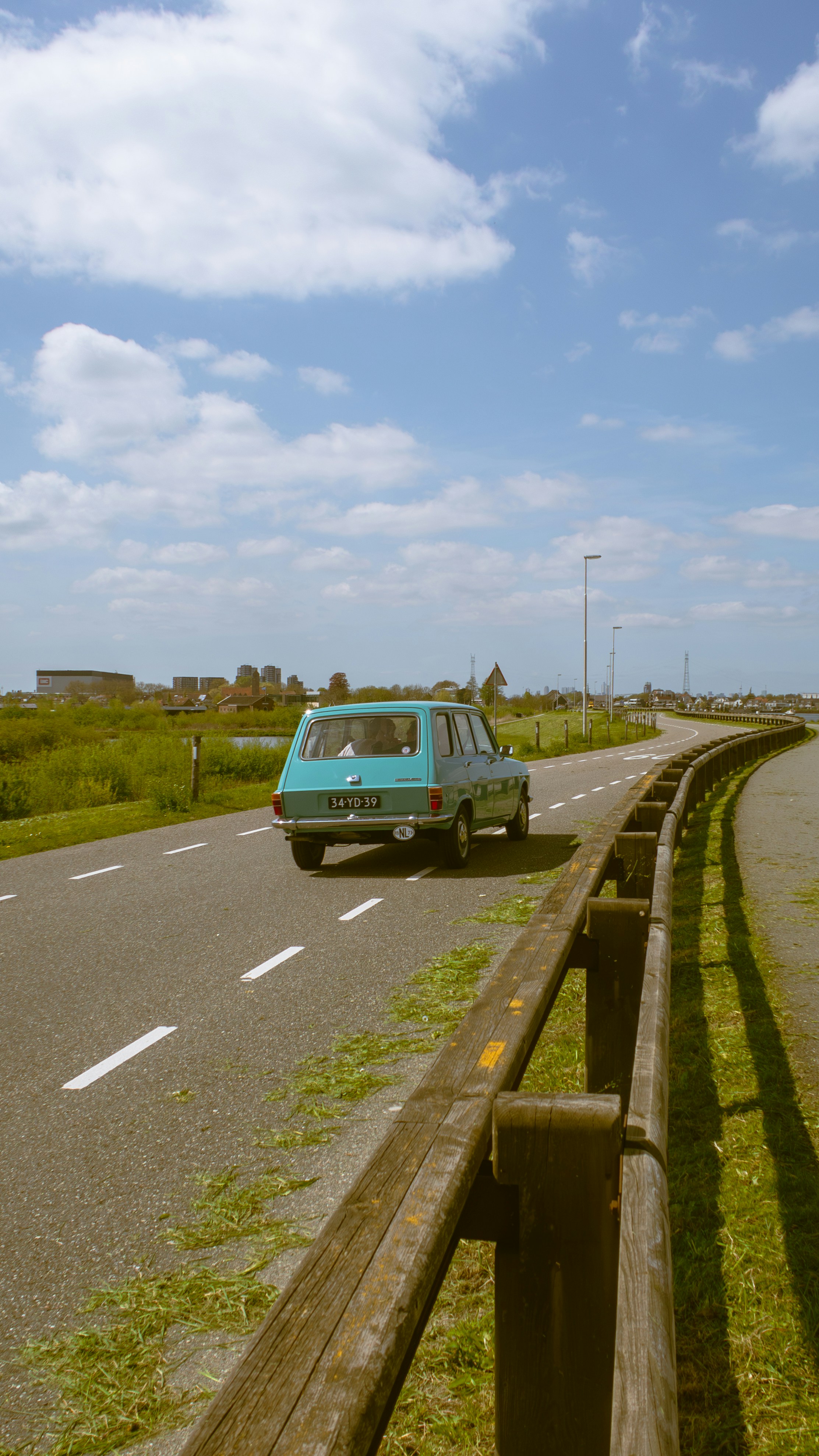 Teal Vintage Car on a Quiet Rural Road by Weathered Guardrail