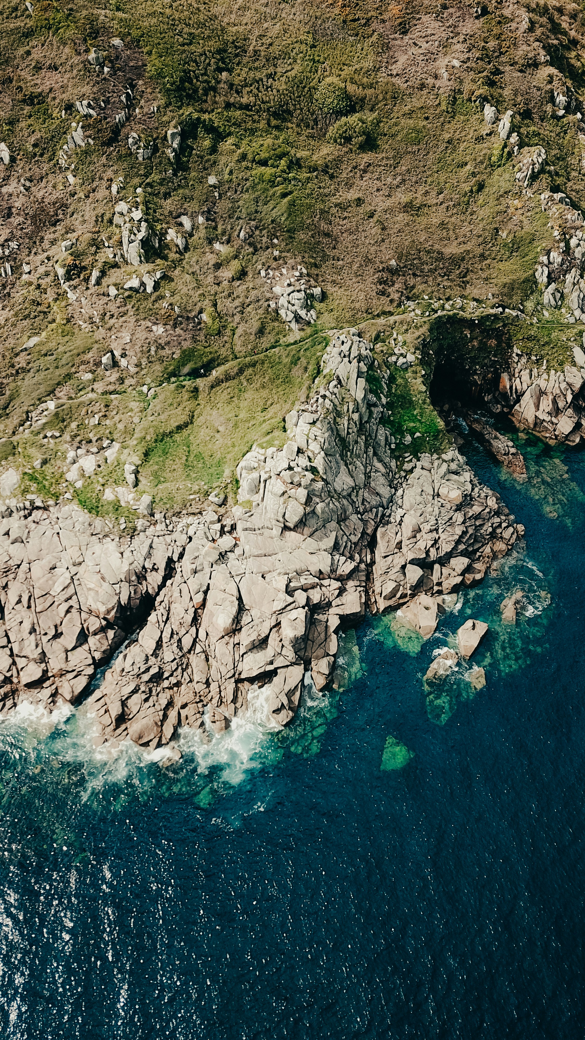 Aerial view of a rugged cliffside meeting the ocean, with vibrant blue waters and jagged rocks.