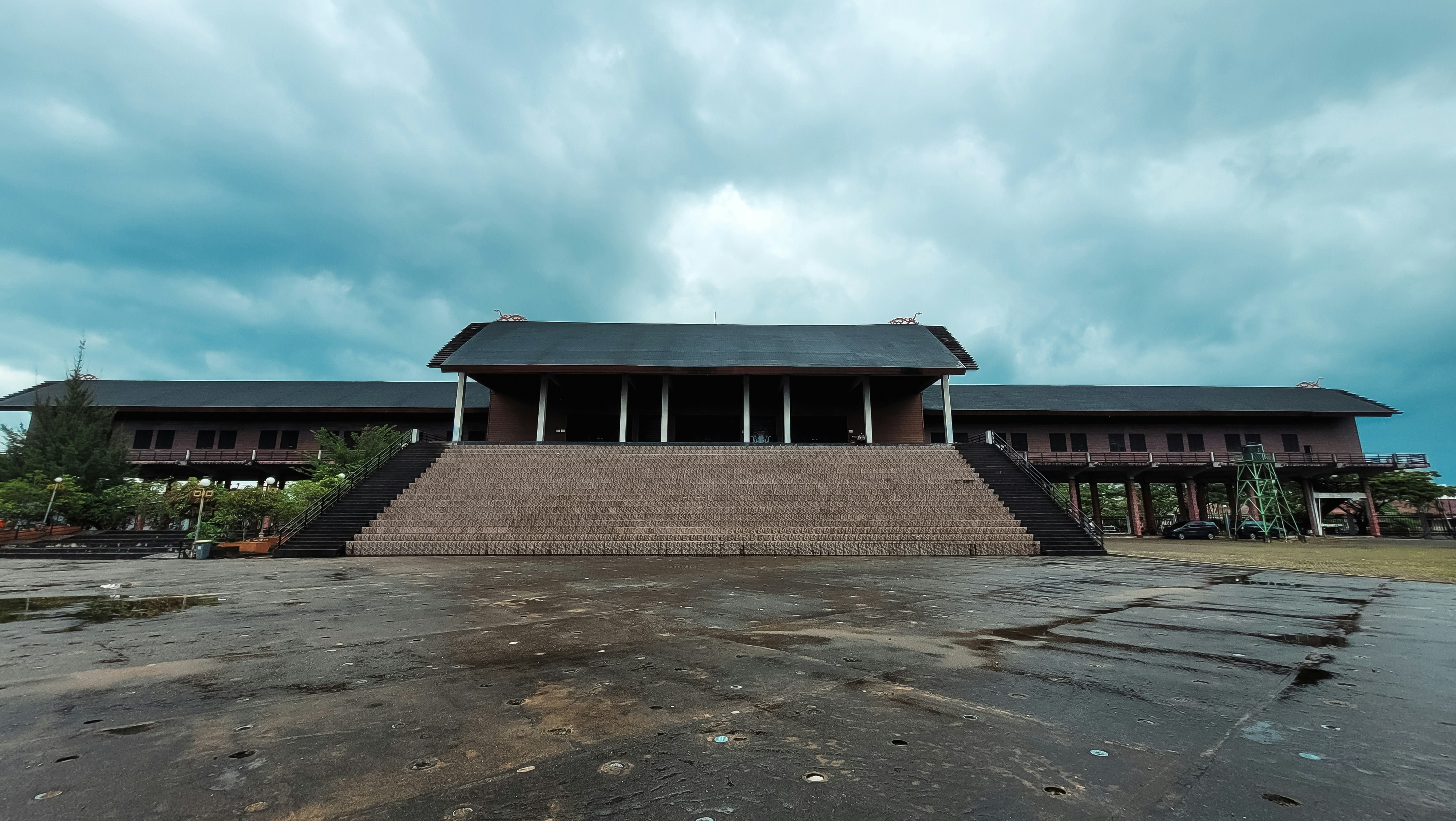 A large, modern building with a prominent staircase set against a dramatic cloudy sky, emphasizing its architectural design.