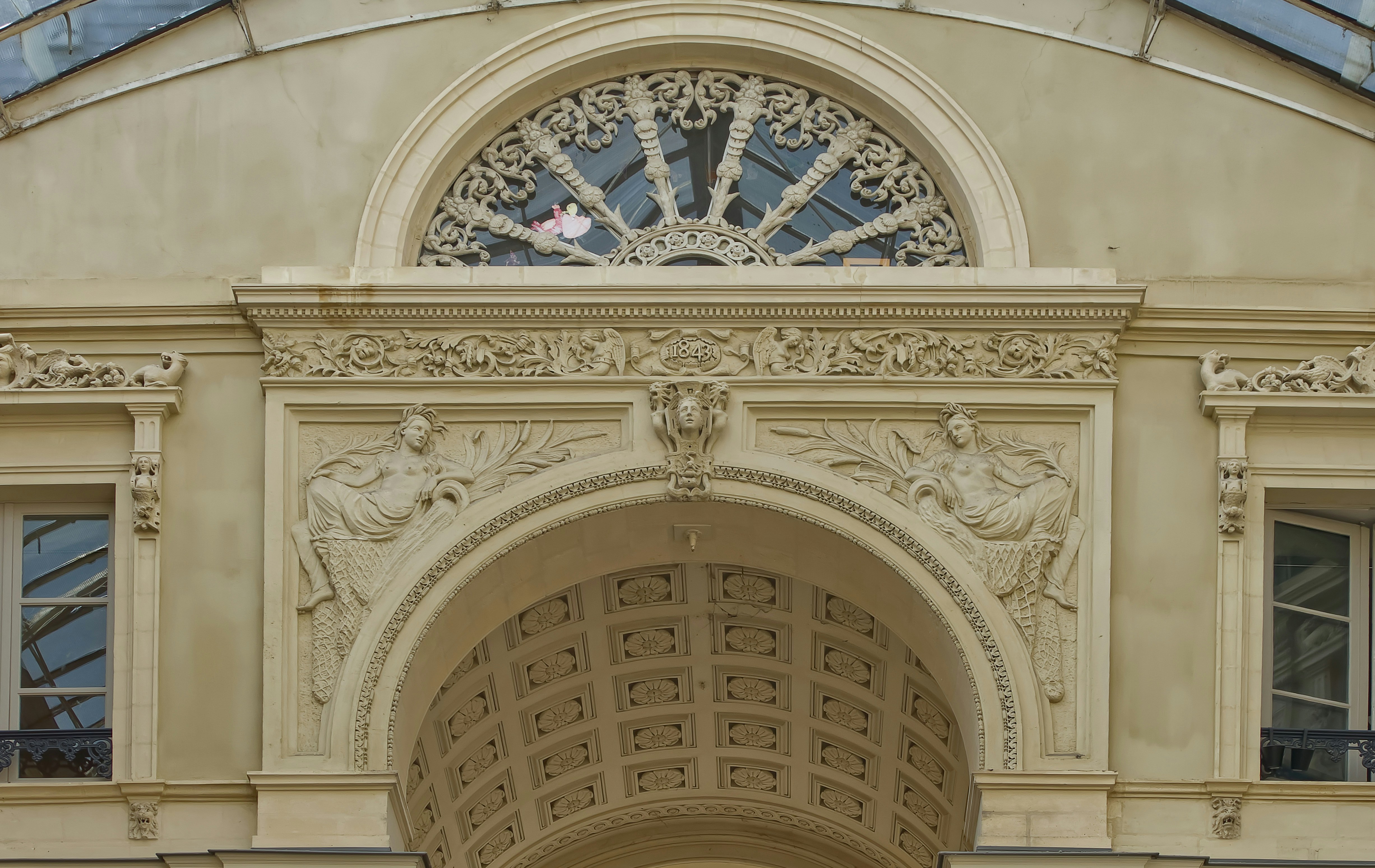 Ornate stone archway featuring intricate carvings beneath a semicircular window with radiating patterns.