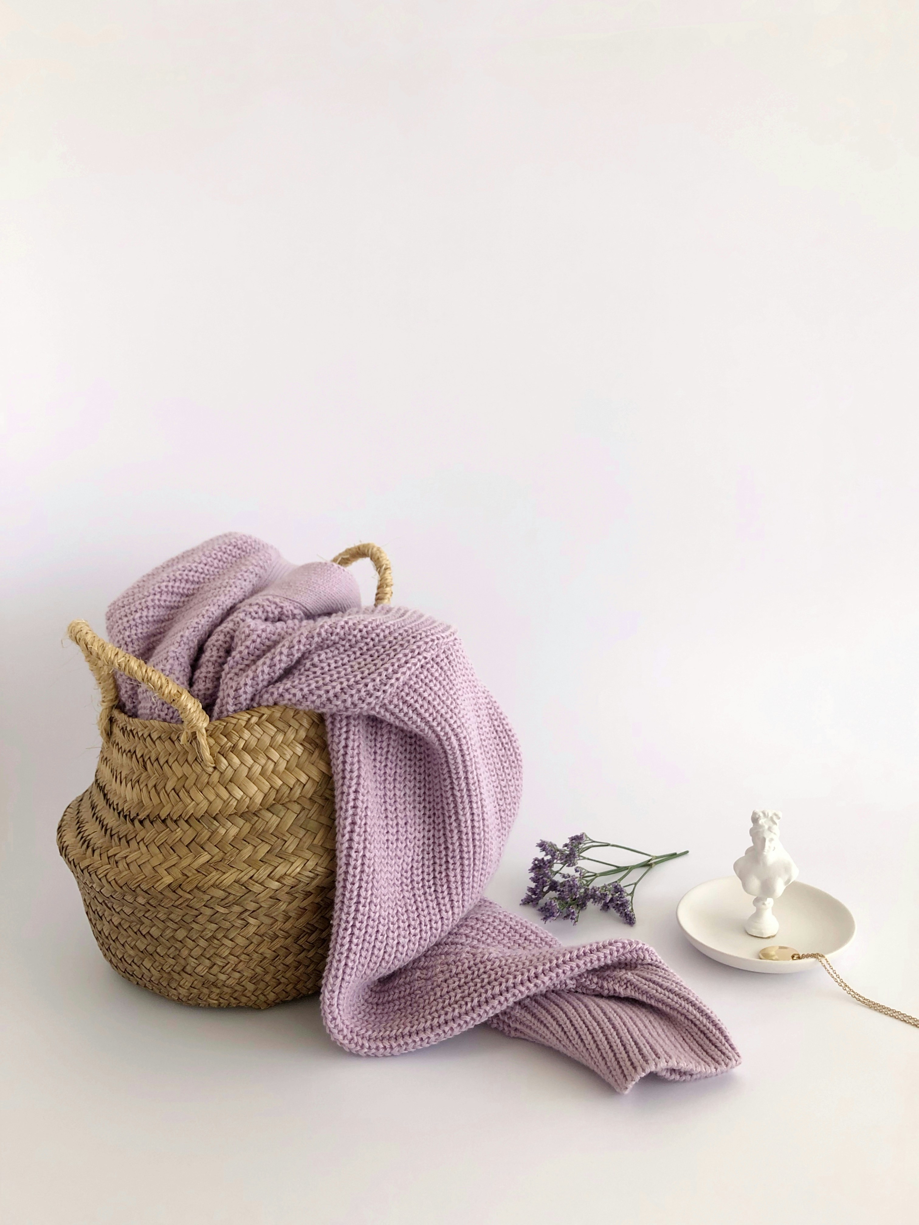 Woven basket filled with a lavender blanket, accompanied by a sprig of lavender and a decorative dish. The gentle hues create a calming atmosphere.