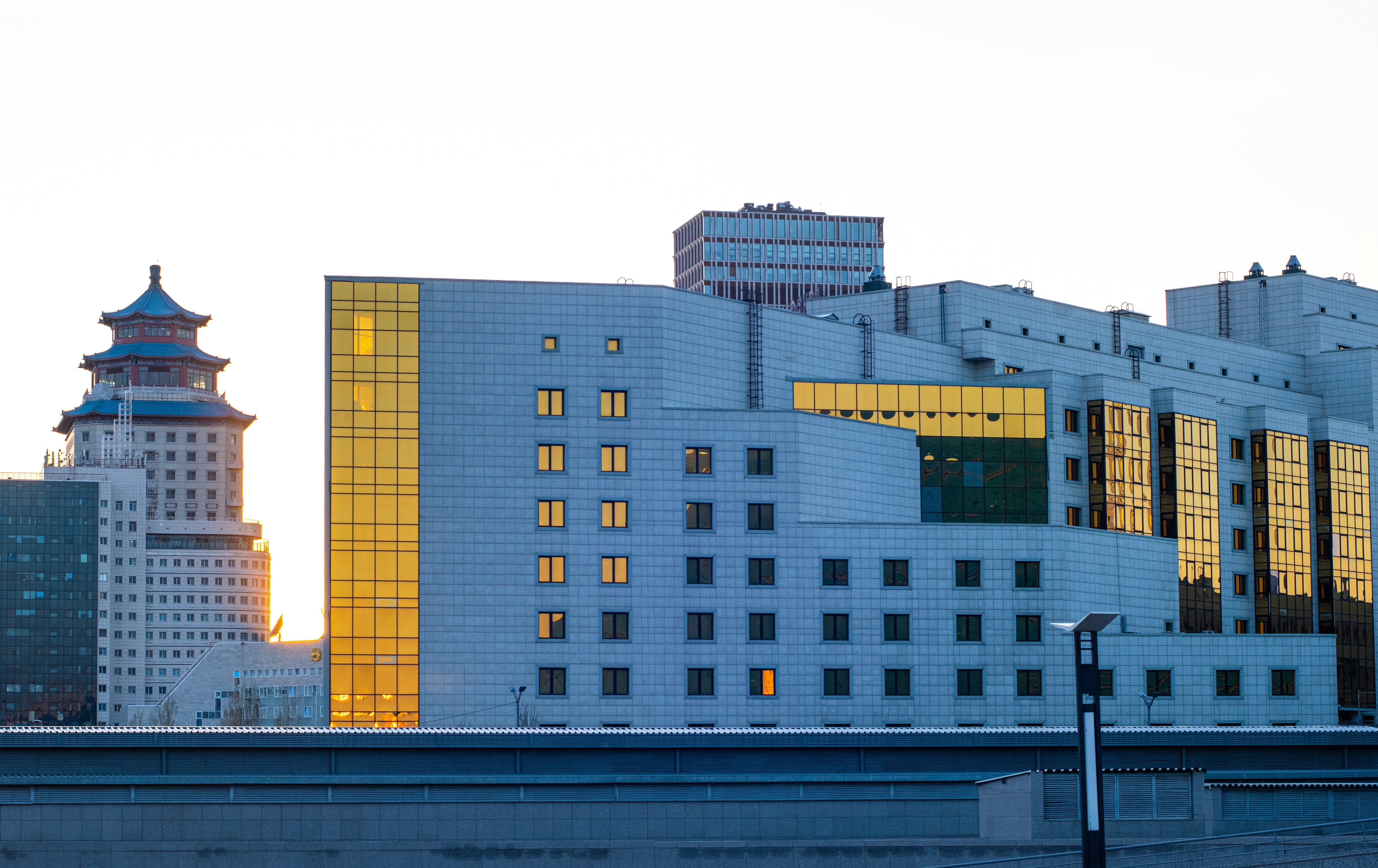 Modern building facade illuminated by sunset, highlighting a pagoda-style structure in the background.
