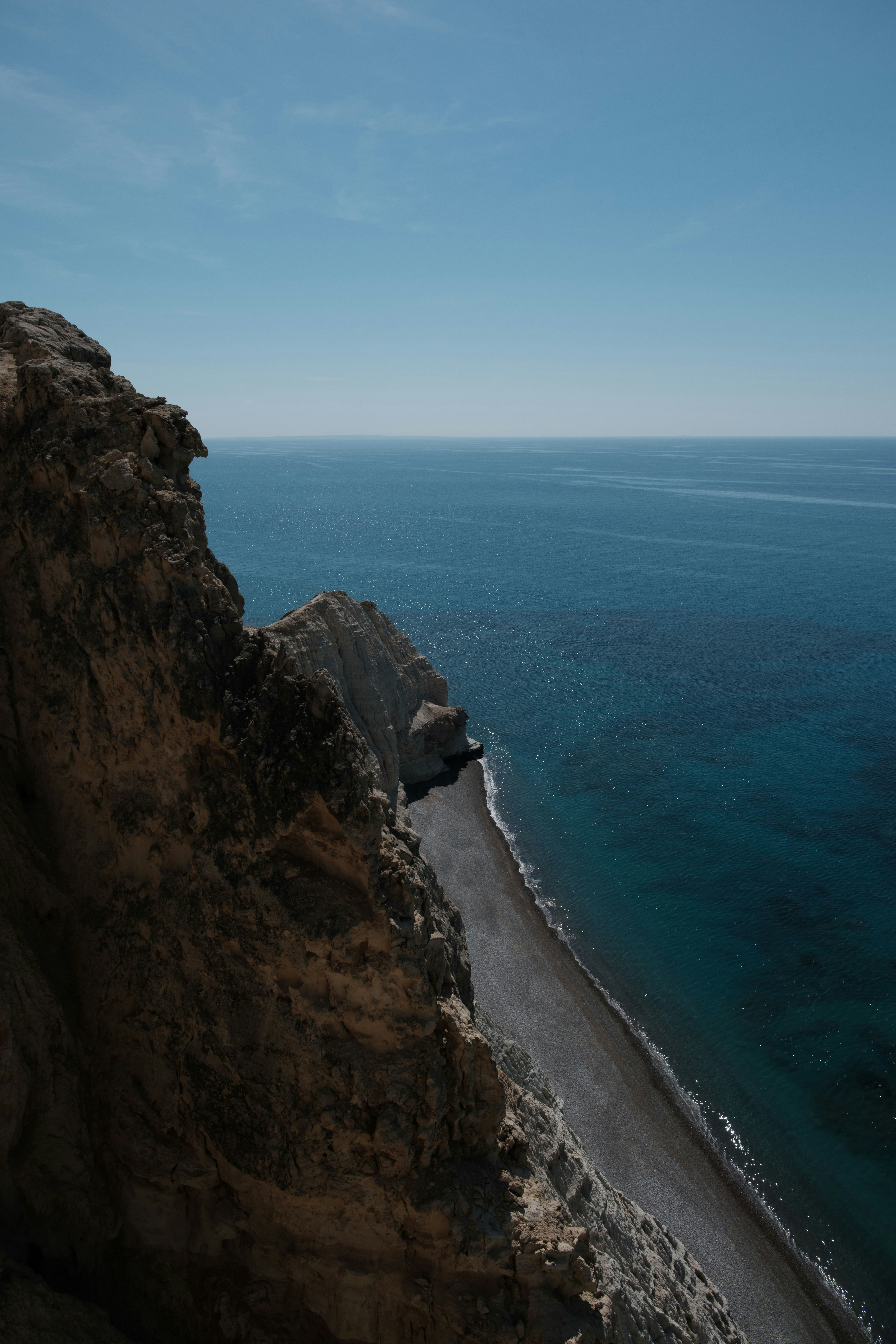 Edge of the Cliff: A Quiet Pebble Beach Beneath a Wide Blue Horizon