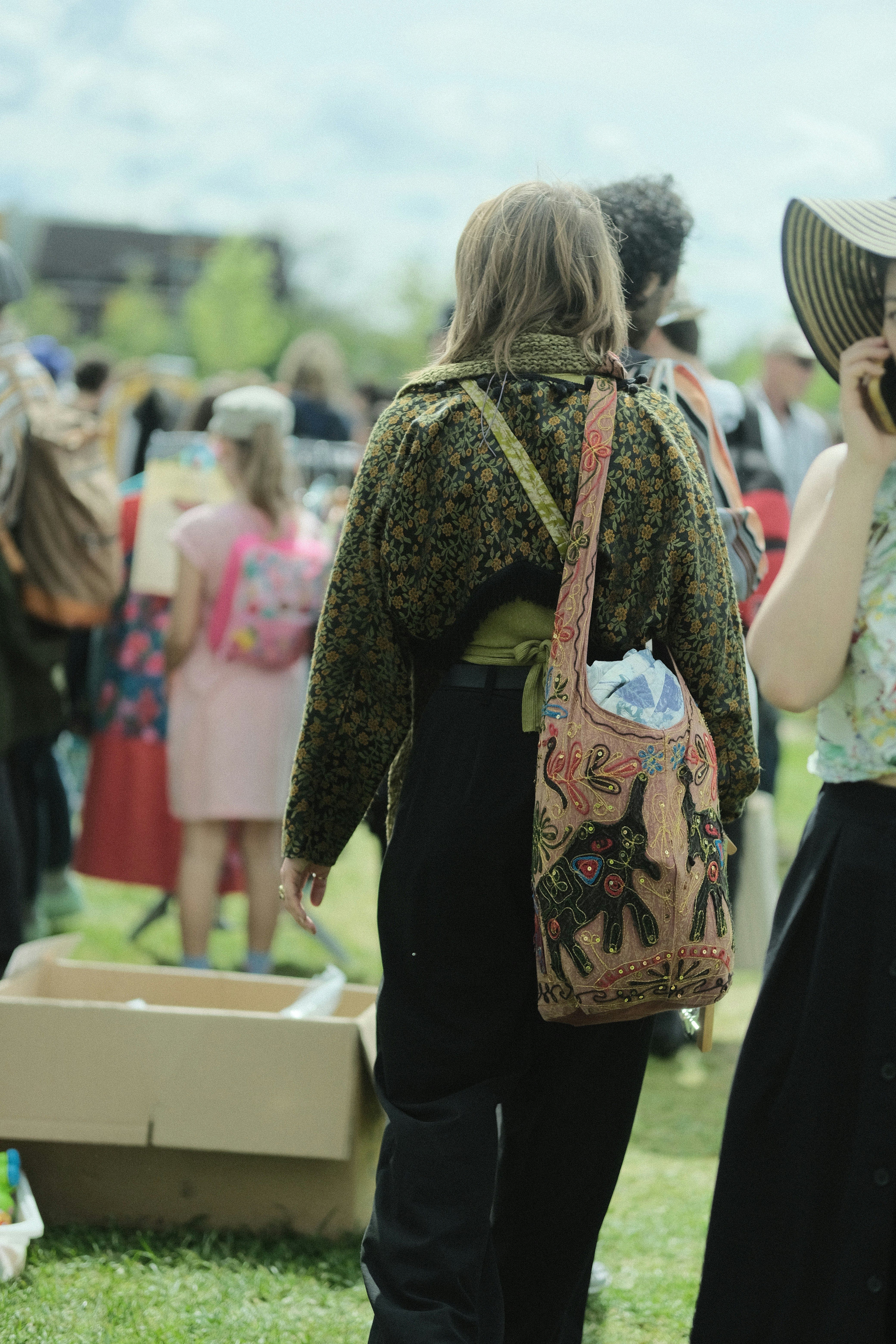 Back-View at a Sunlit Festival: Floral Jacket, Elephant Tote, and a Curious Crowd
