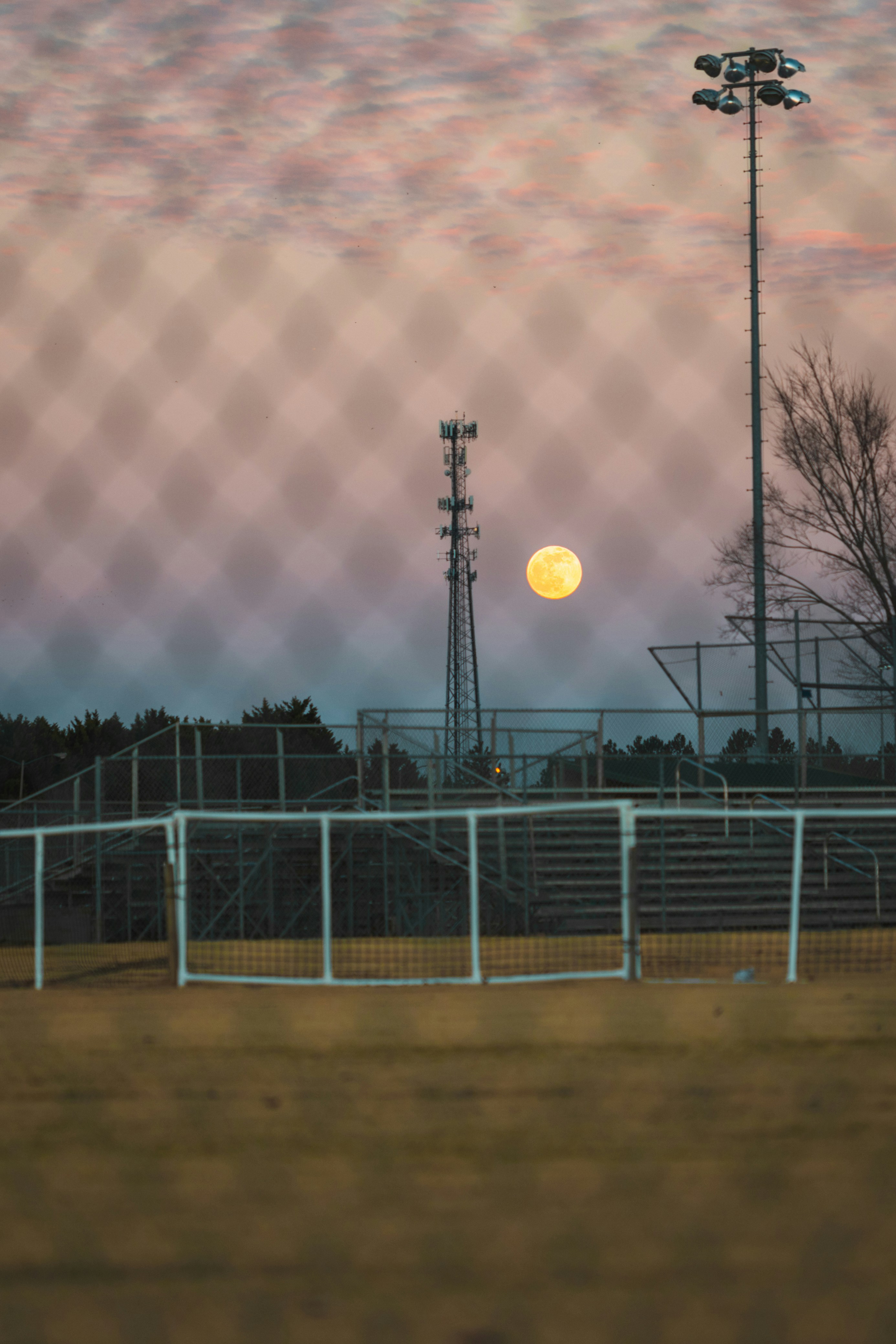Moonrise Over the Empty Field: Fences, Floodlights, and a Quiet Dusk