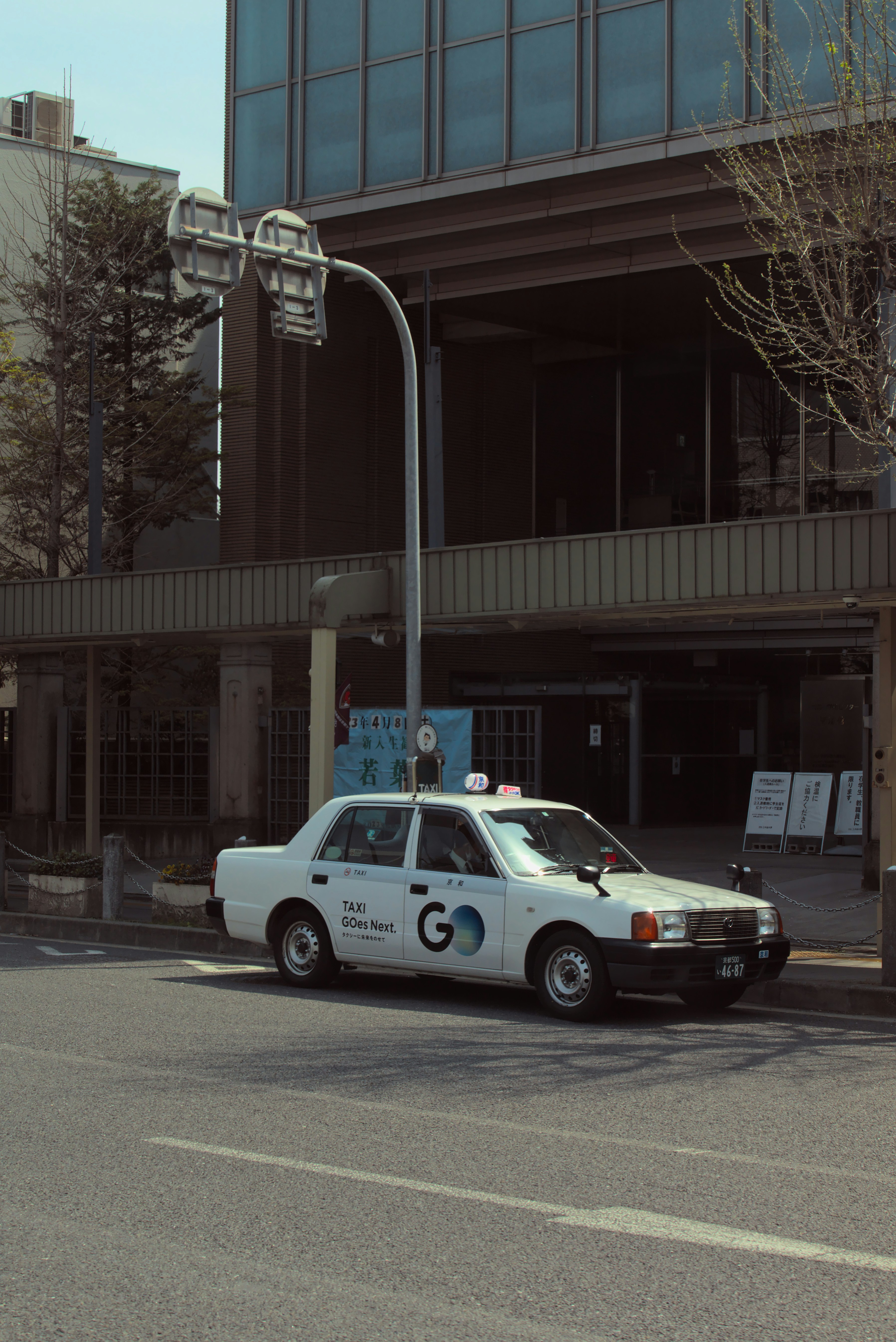 A white taxi cab driving down a street next to a tall building photo ...