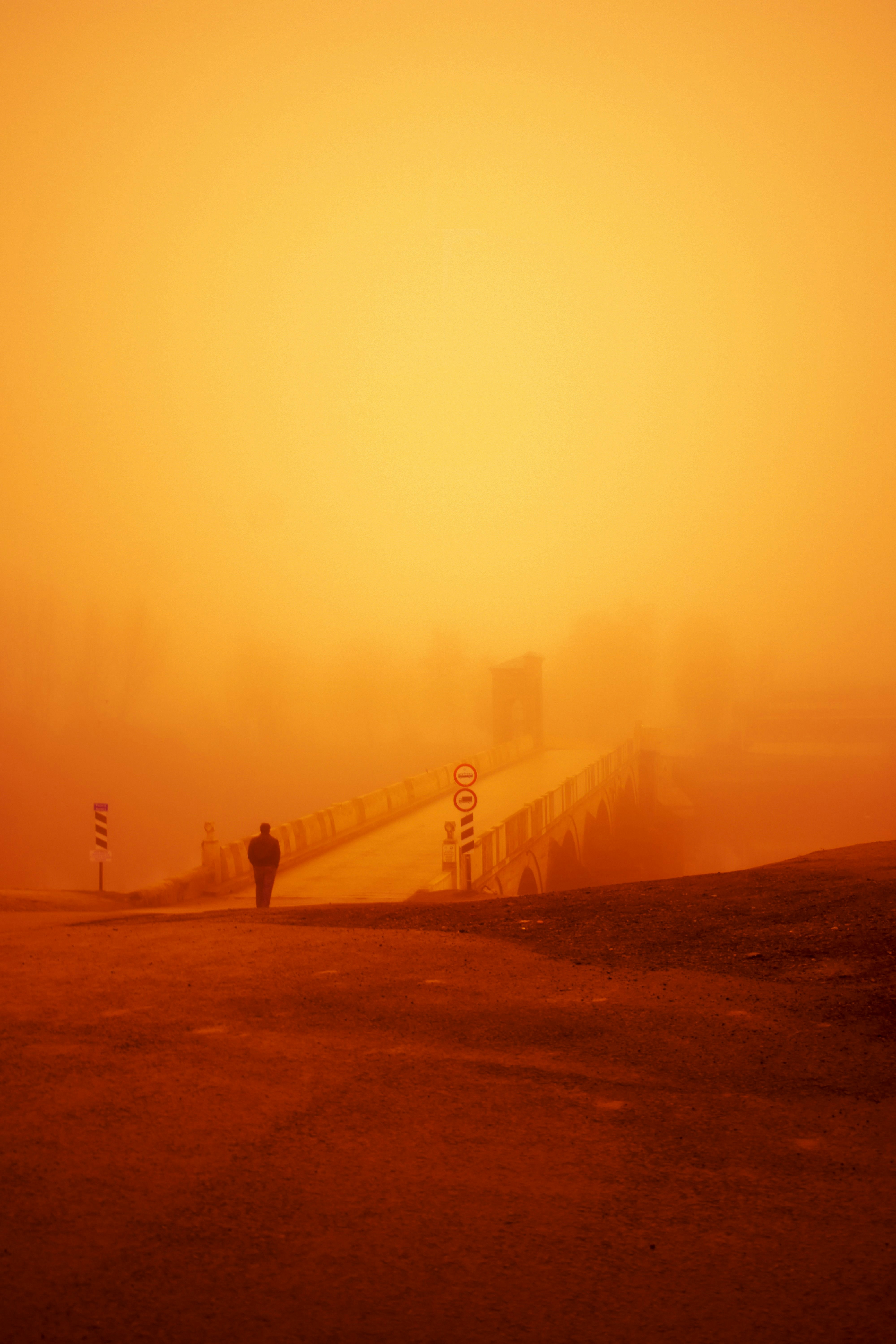 A man walking alone on a foggy road to a historic Ottoman bridge with his hands in his pockets.