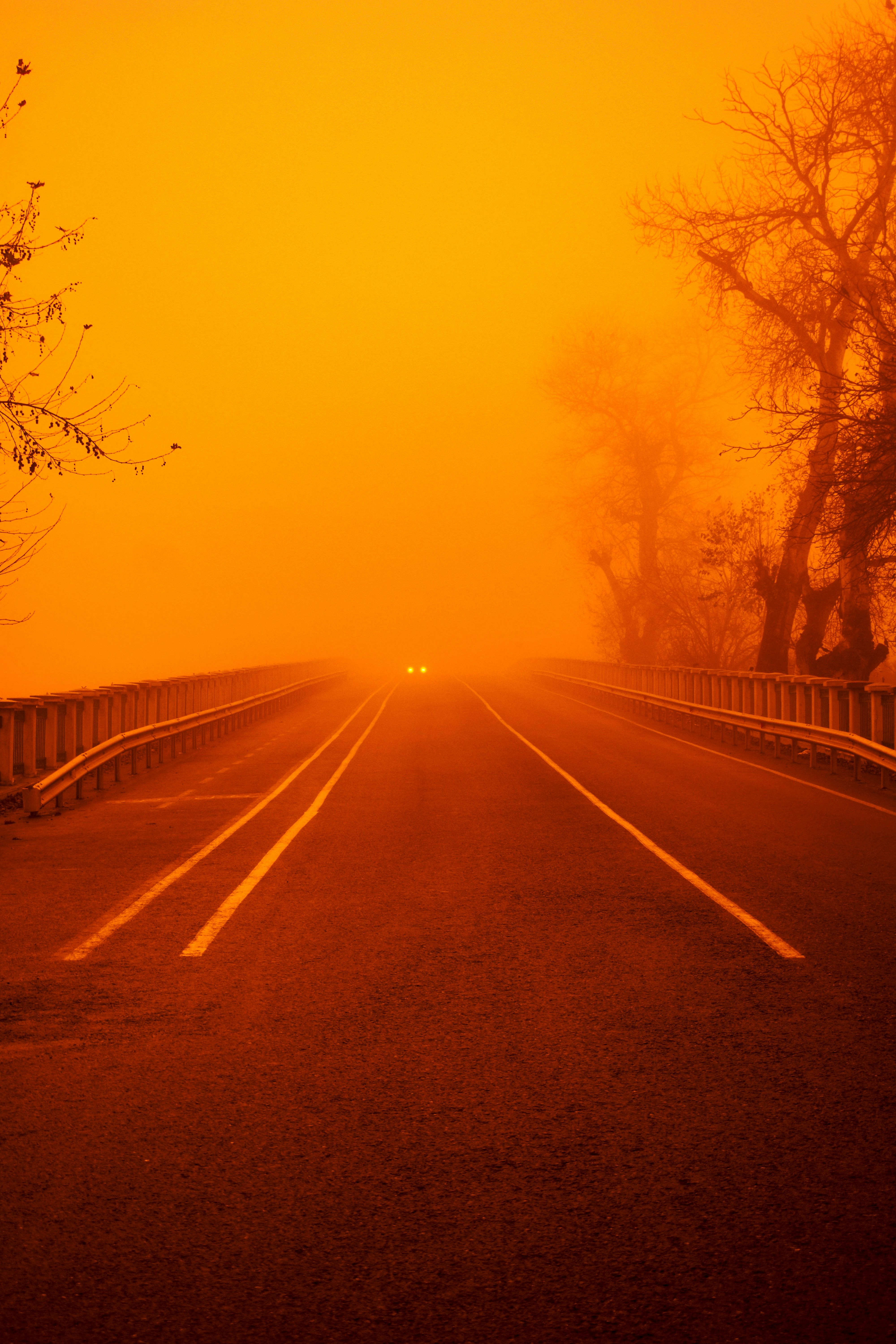 A car with only headlights visible in the fog.