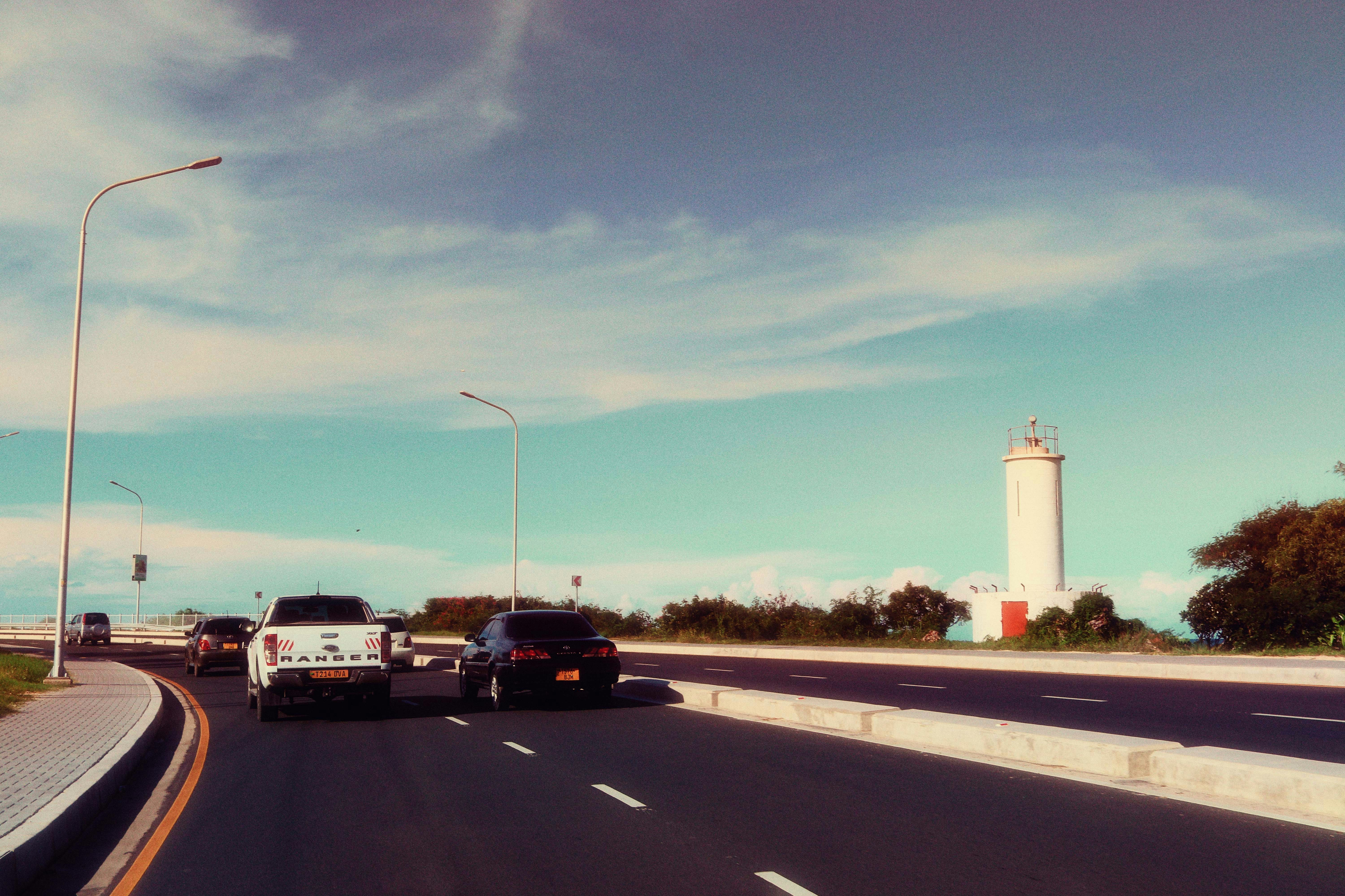 Two vehicles travel on a wide highway under a bright blue sky with scattered clouds.