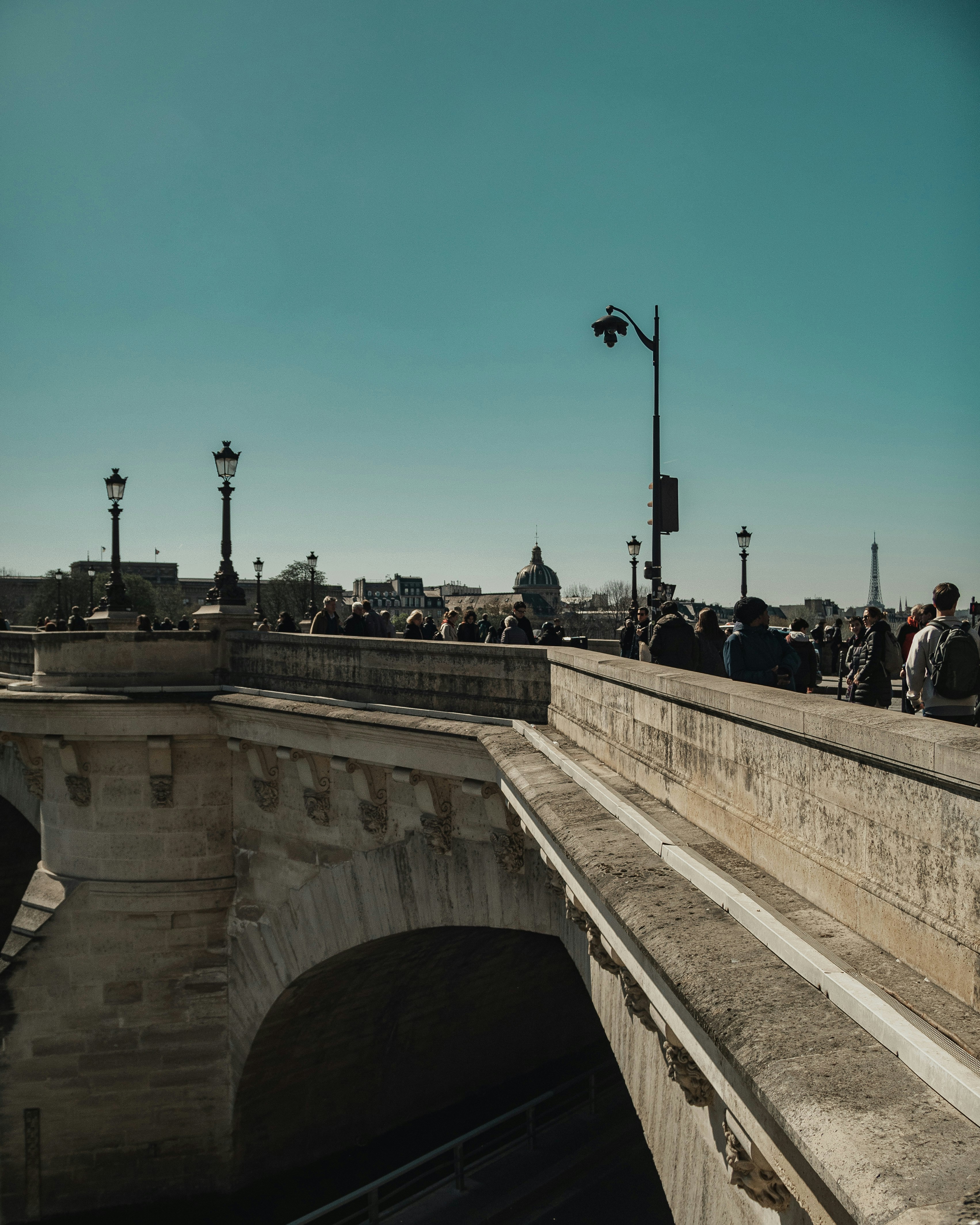 Cerulean Sky Over a Crowded Stone Bridge Promenade