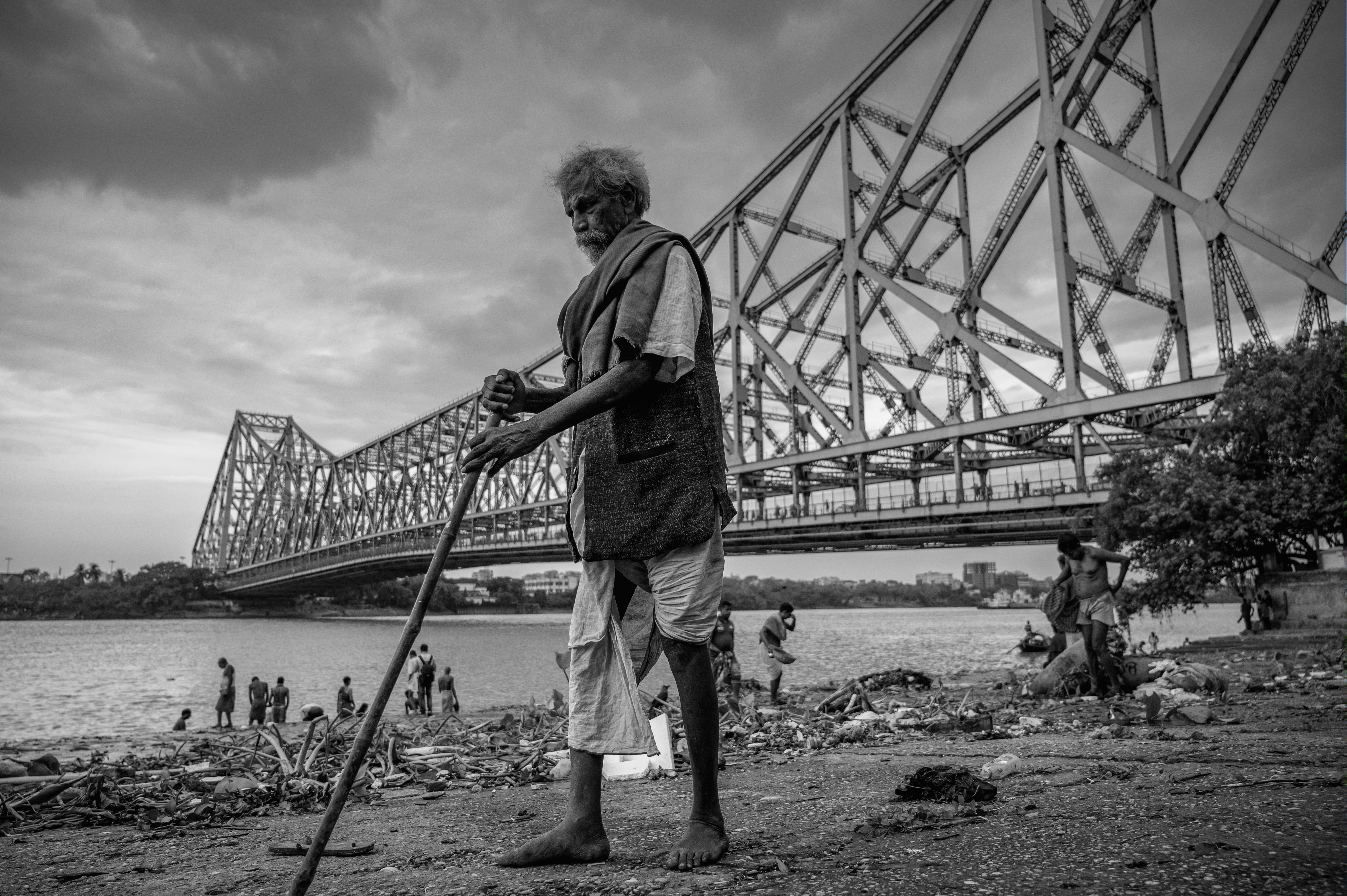 A Lone Walker Beneath a Steel Spine: Quiet Strength on the Riverbank