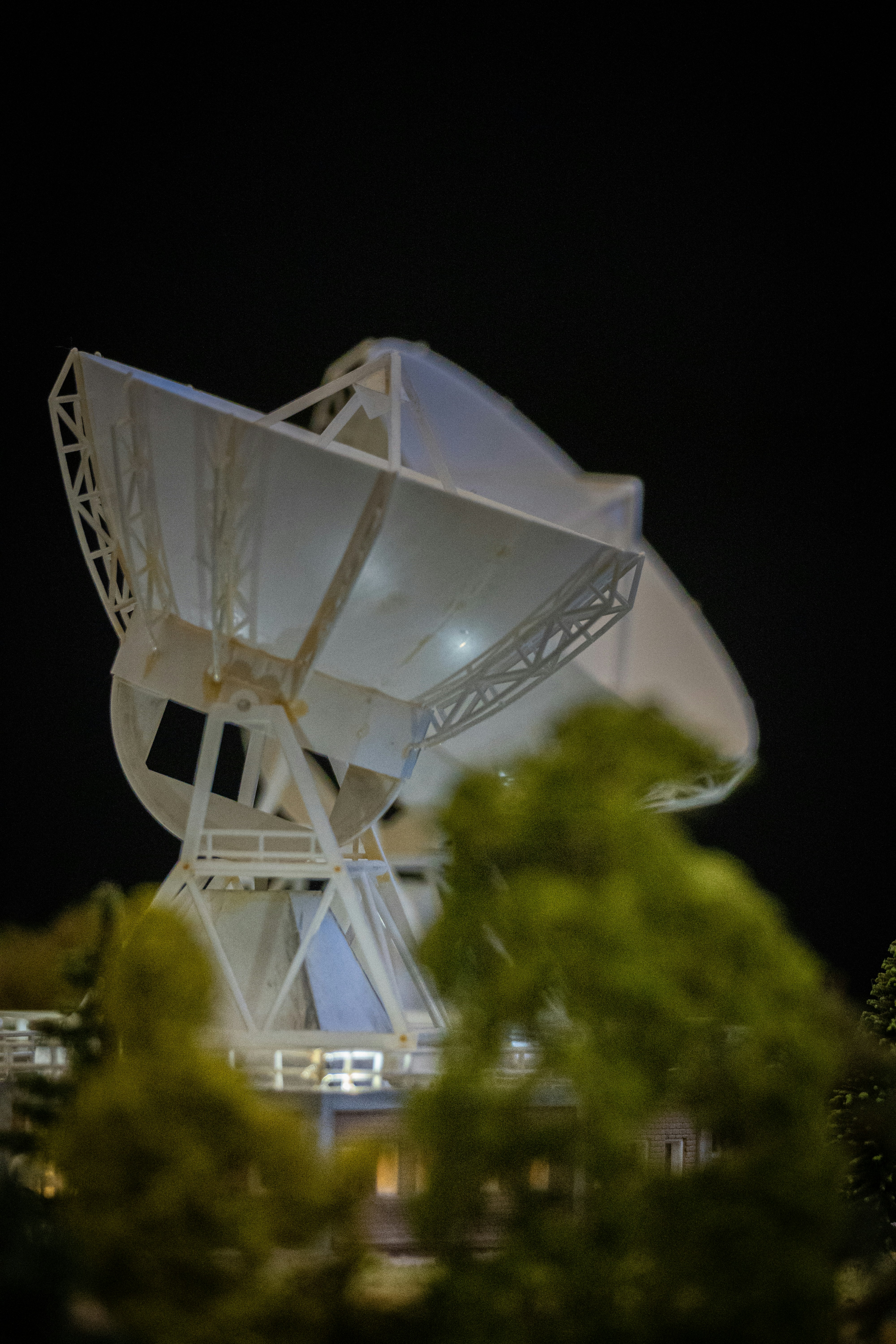Large satellite dish structure illuminated against a night sky, surrounded by greenery. The design emphasizes modern technology in a natural setting.