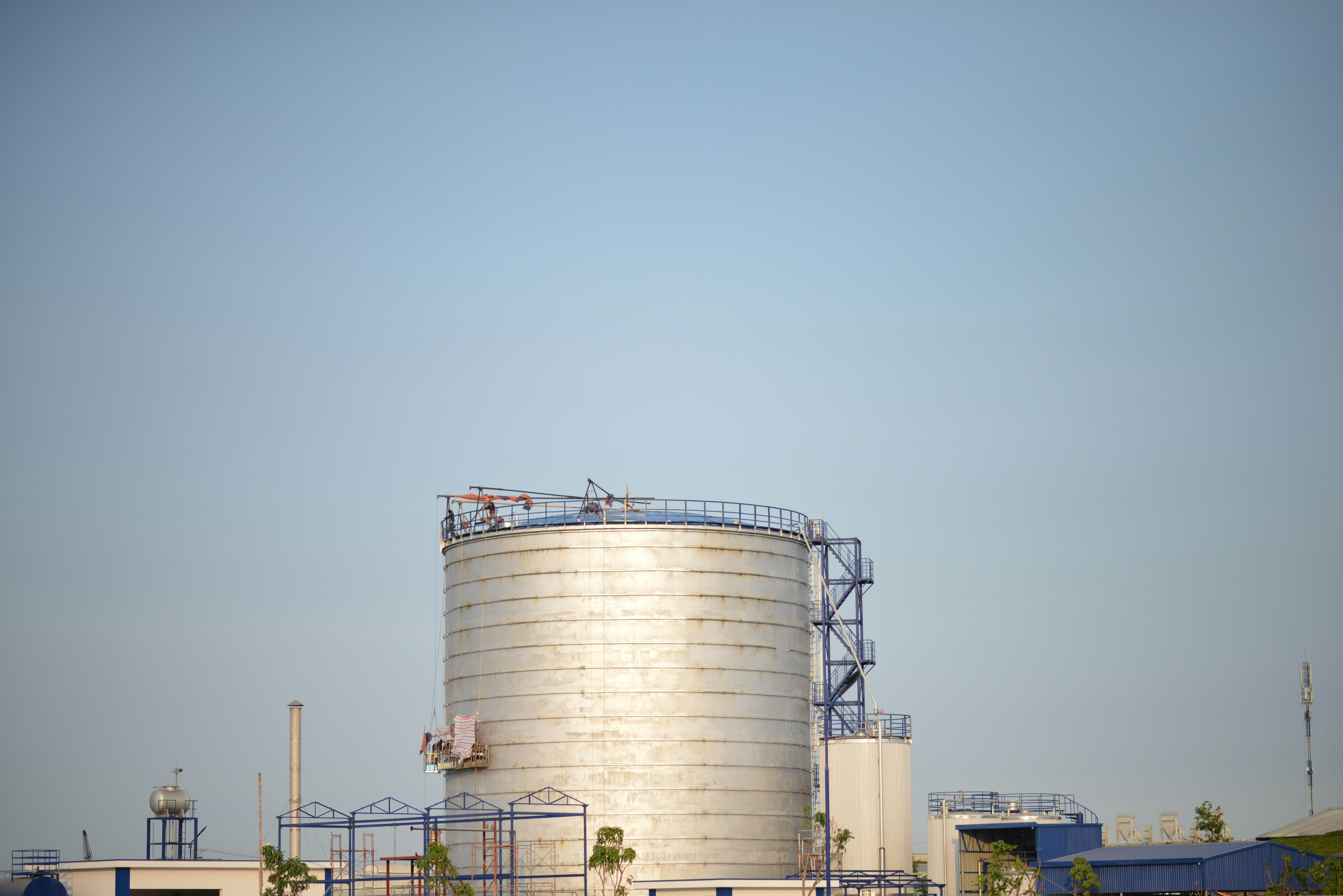 Large metallic storage tank with surrounding industrial structures under a clear blue sky.