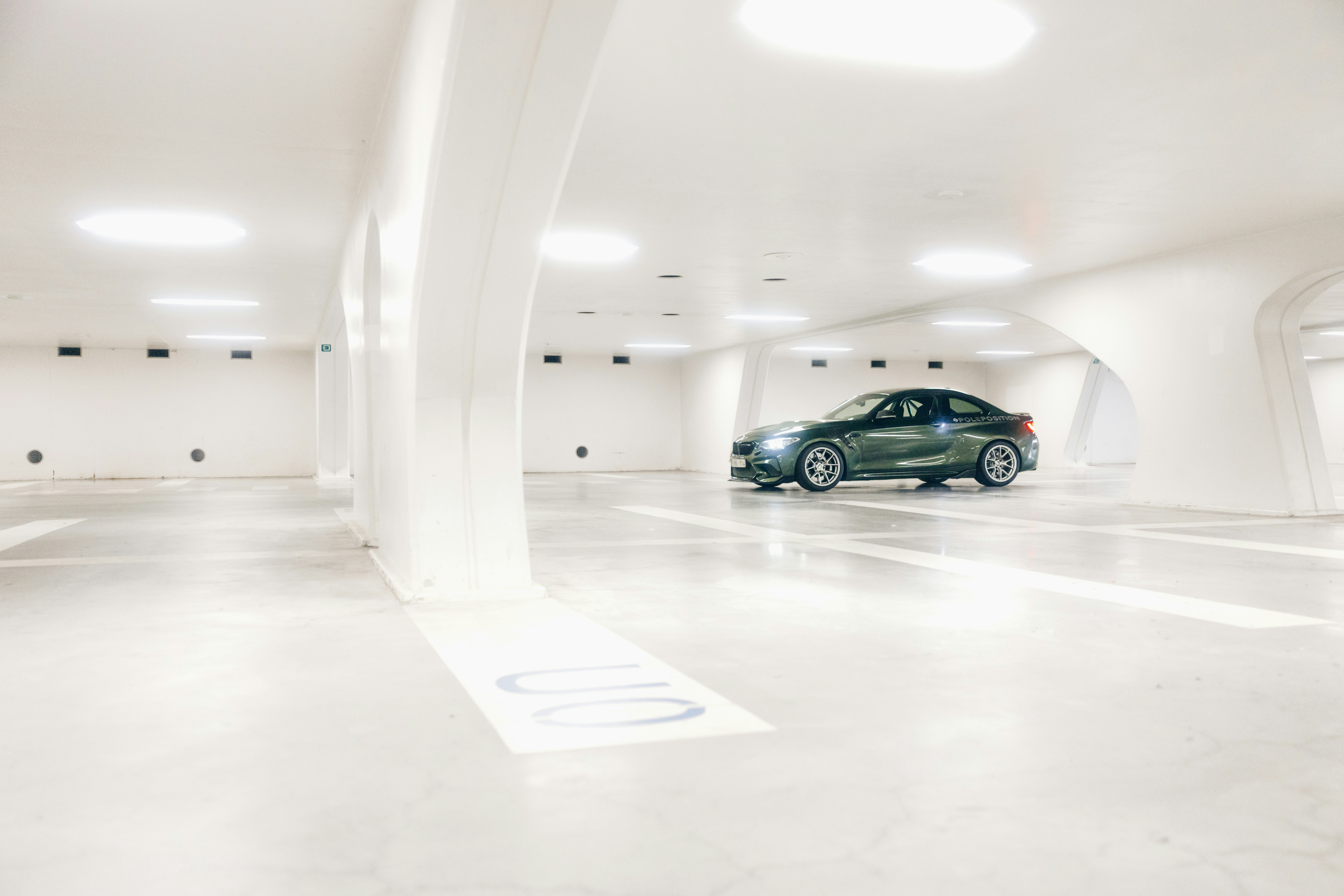 A green car parked in a white parking garage photo – Free Floor Image ...