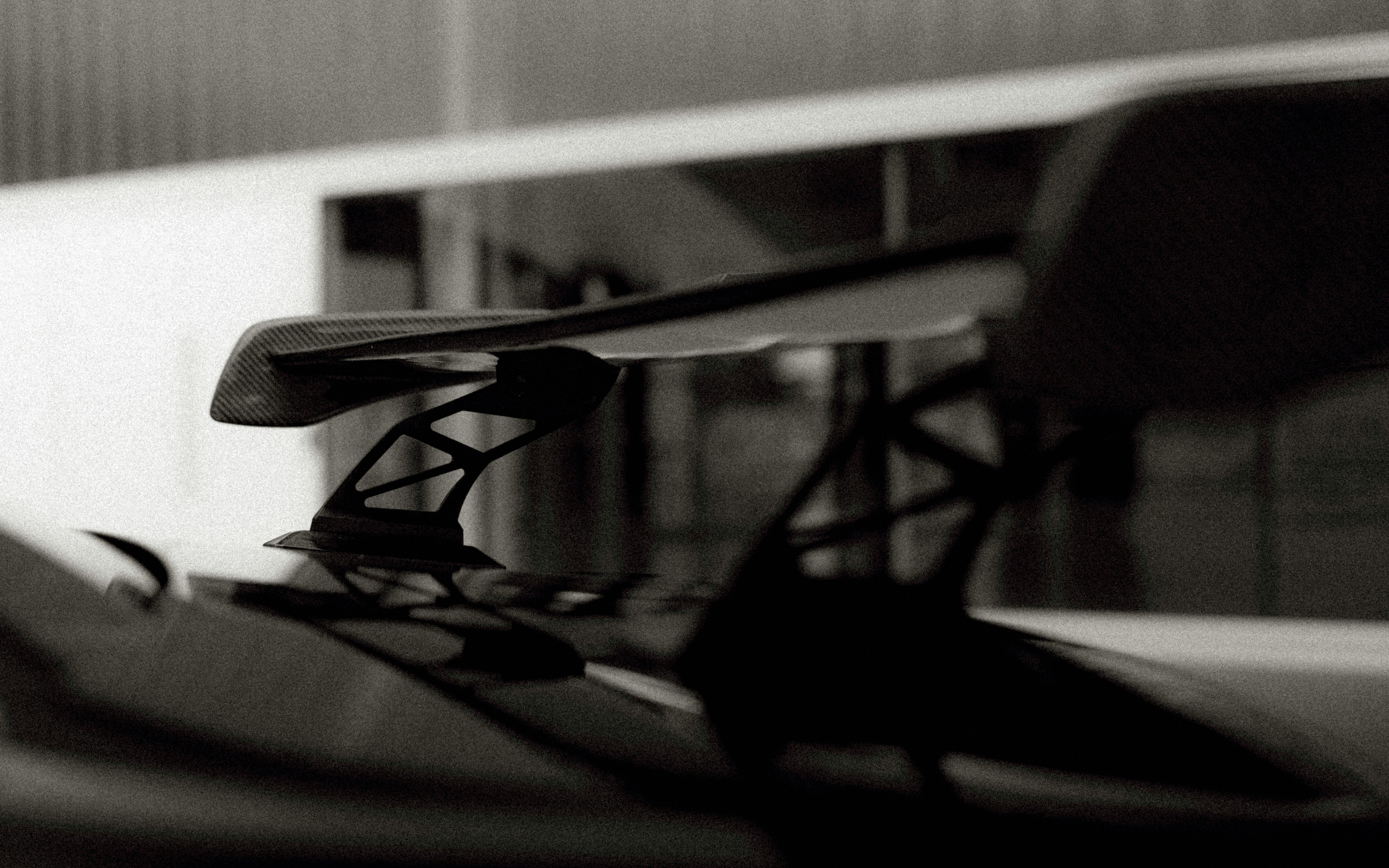 Close-up of a car's rear wing, showcasing sleek lines and shadows in a modern setting.