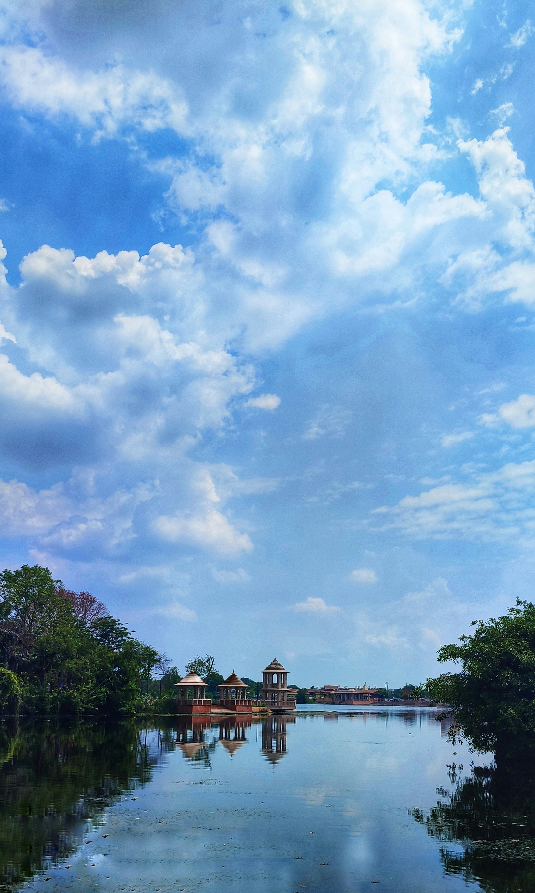 Tranquil lakeside scene with pagoda-style pavilions reflected in still water beneath a bright blue sky.