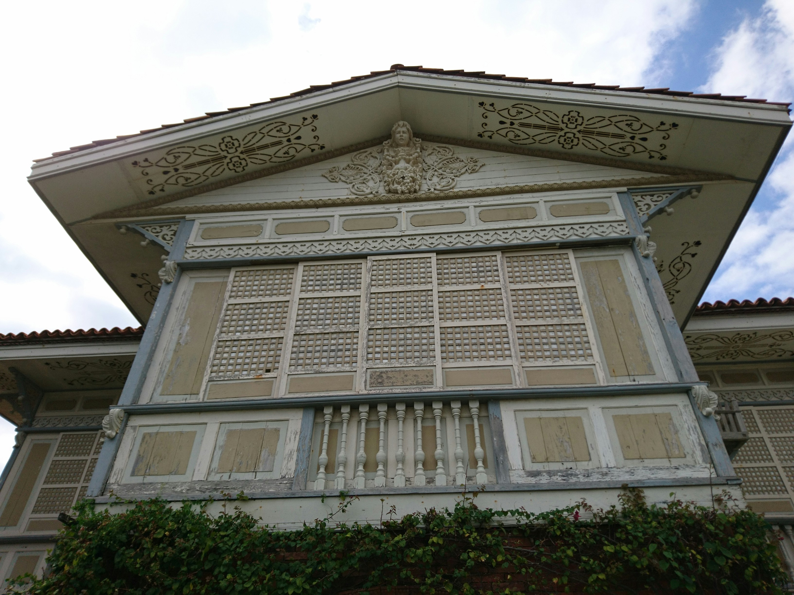 Historic wooden-facade house with lattice panels, balconies, and ivy along the base.